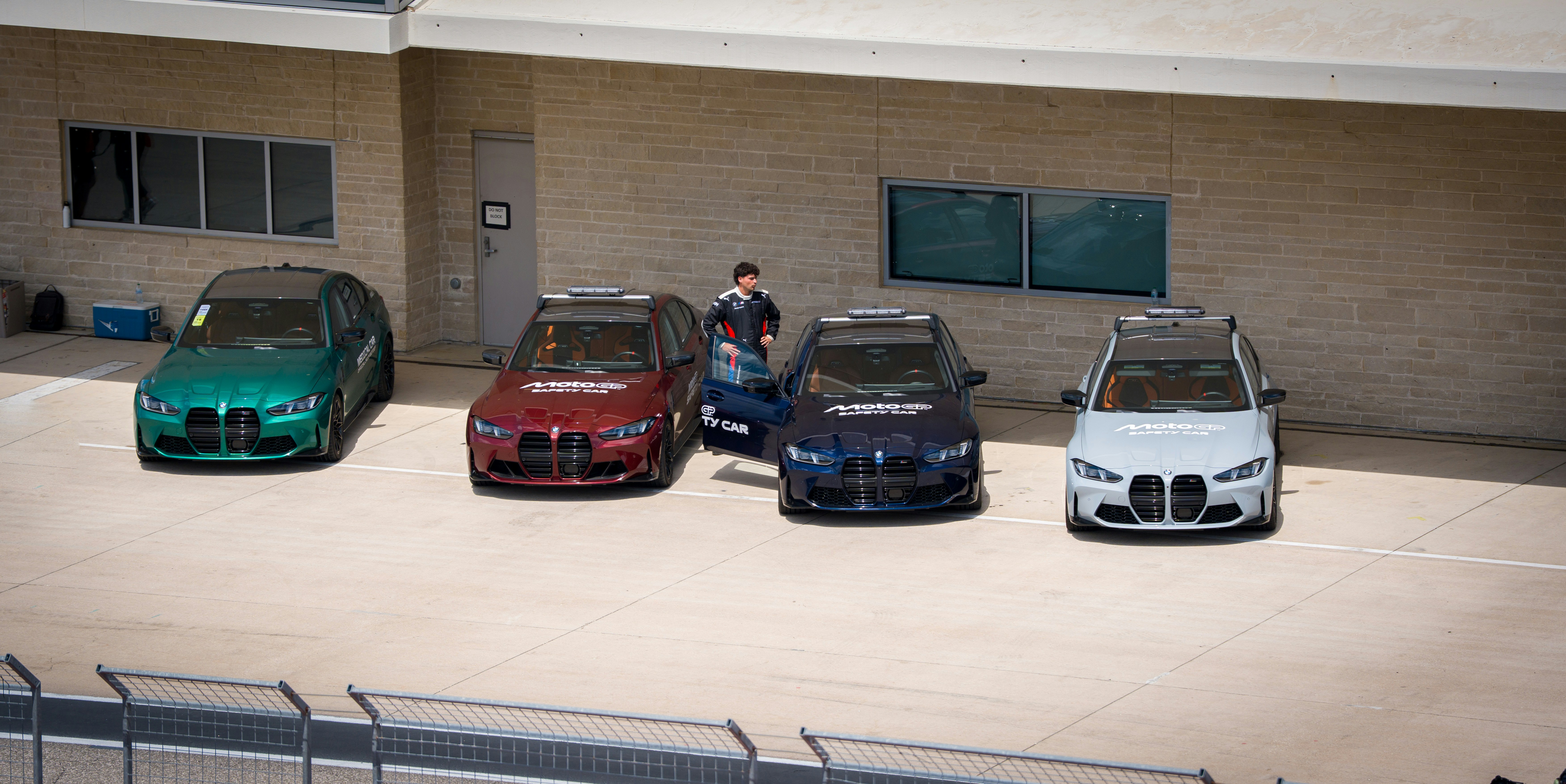 Row of vibrant BMW M models and a display man outside a service bay
