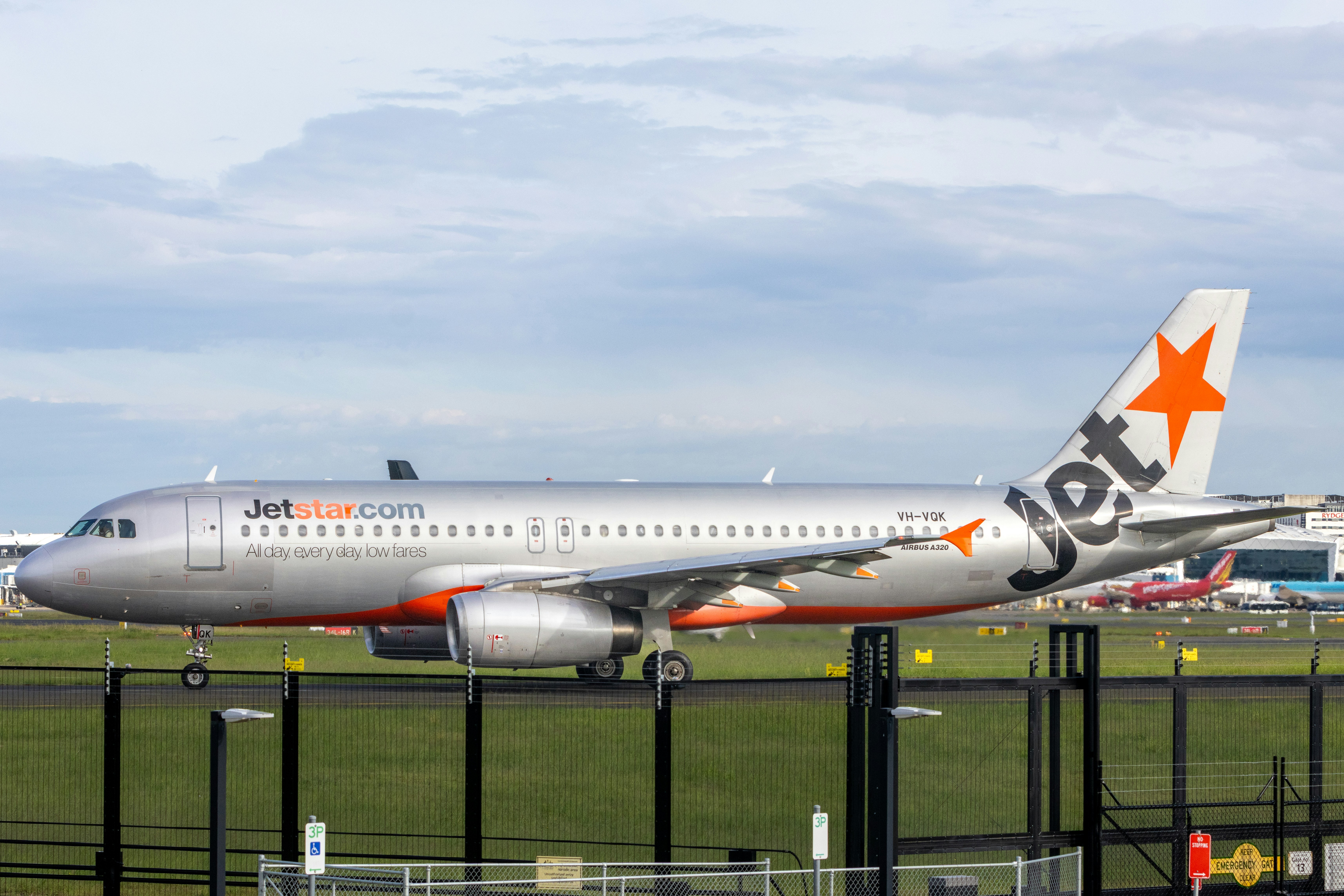 Jetstar at the Fence: A side view of a silver airliner on an airport tarmac