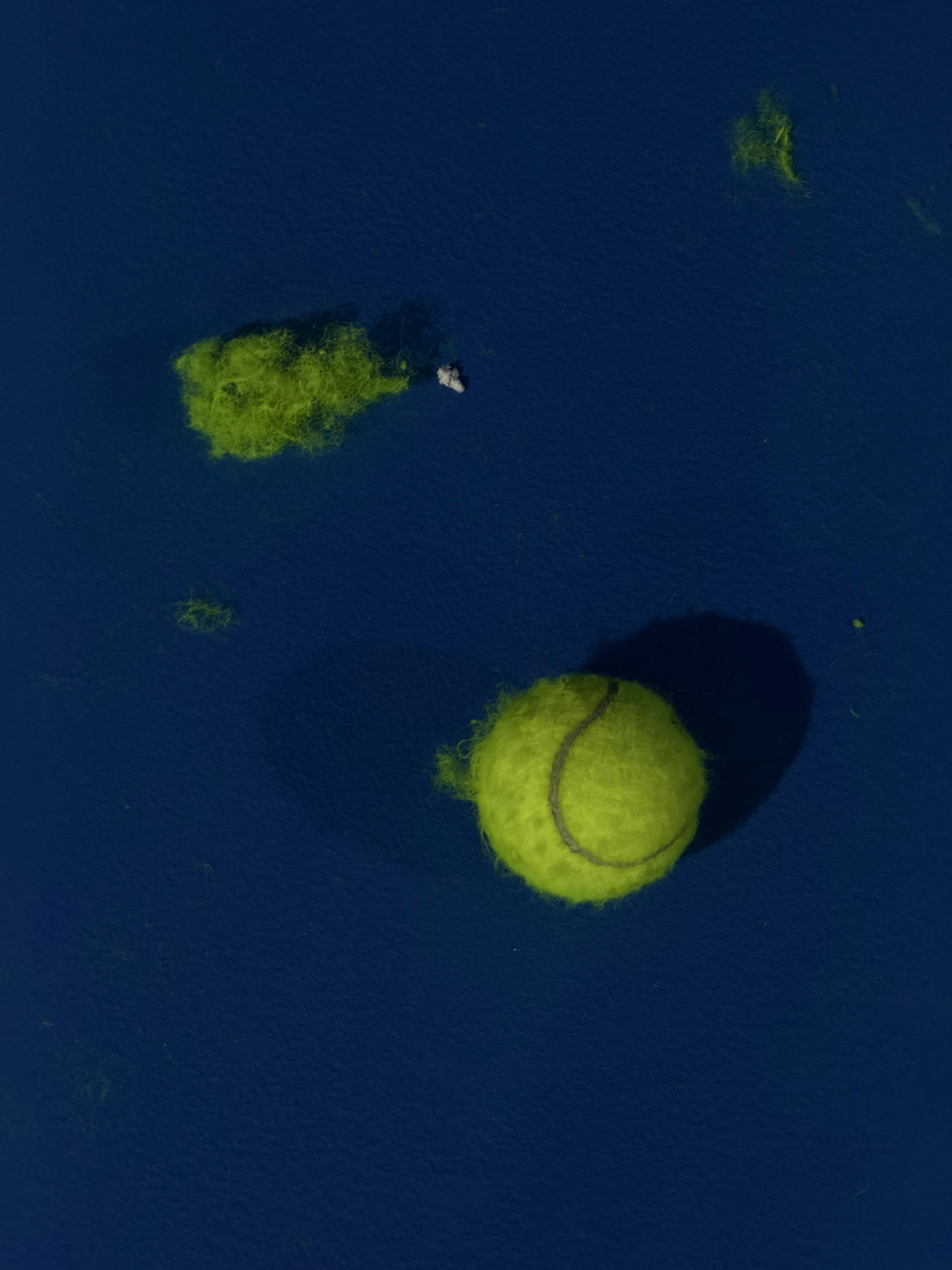 Two Tennis Balls and Debris on a Deep Blue Court