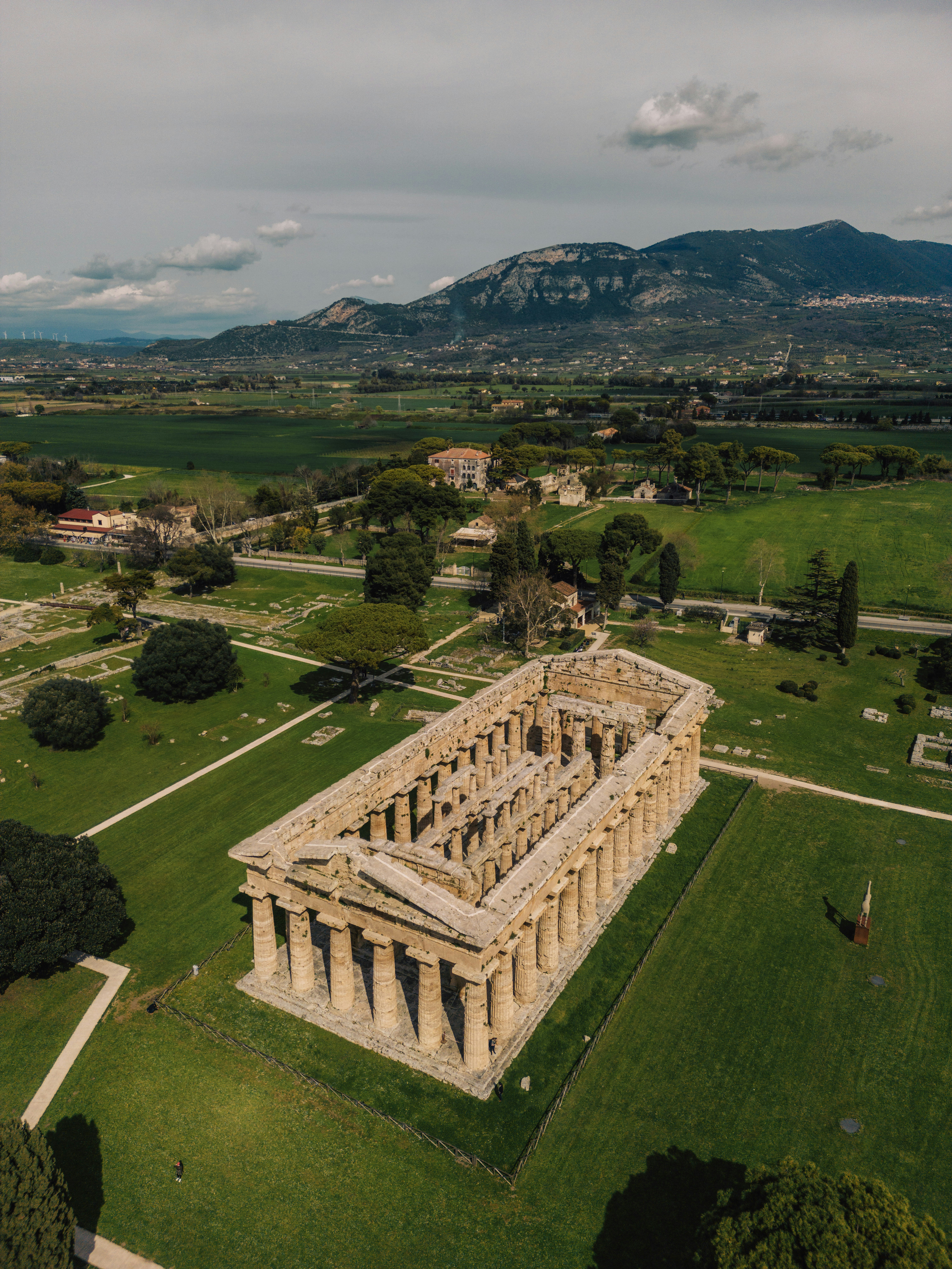 Aerial view of a Roman temple ruin set in a manicured park with distant mountains