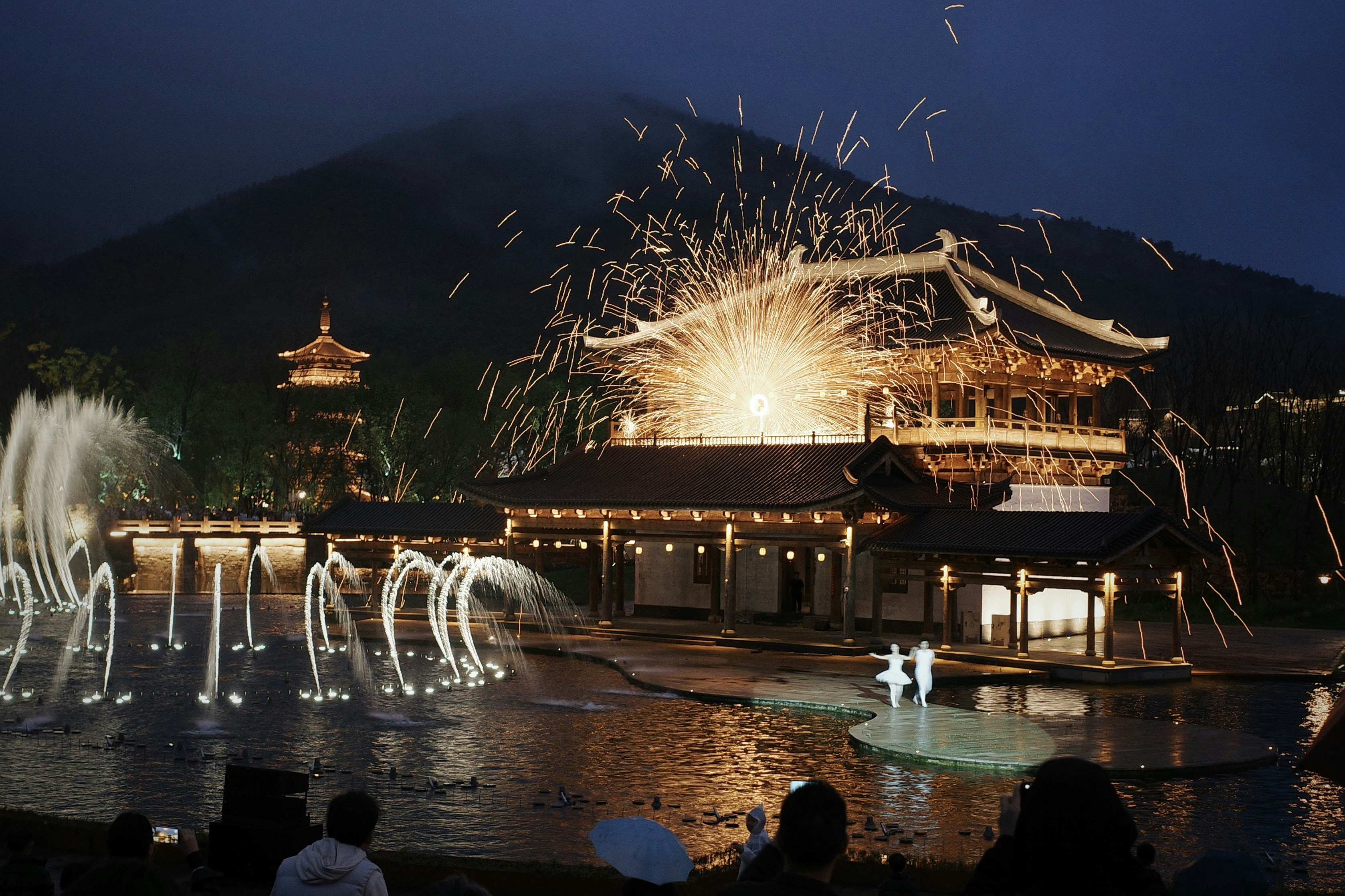 Fireworks over the lit pagoda: night scene on a traditional temple pond