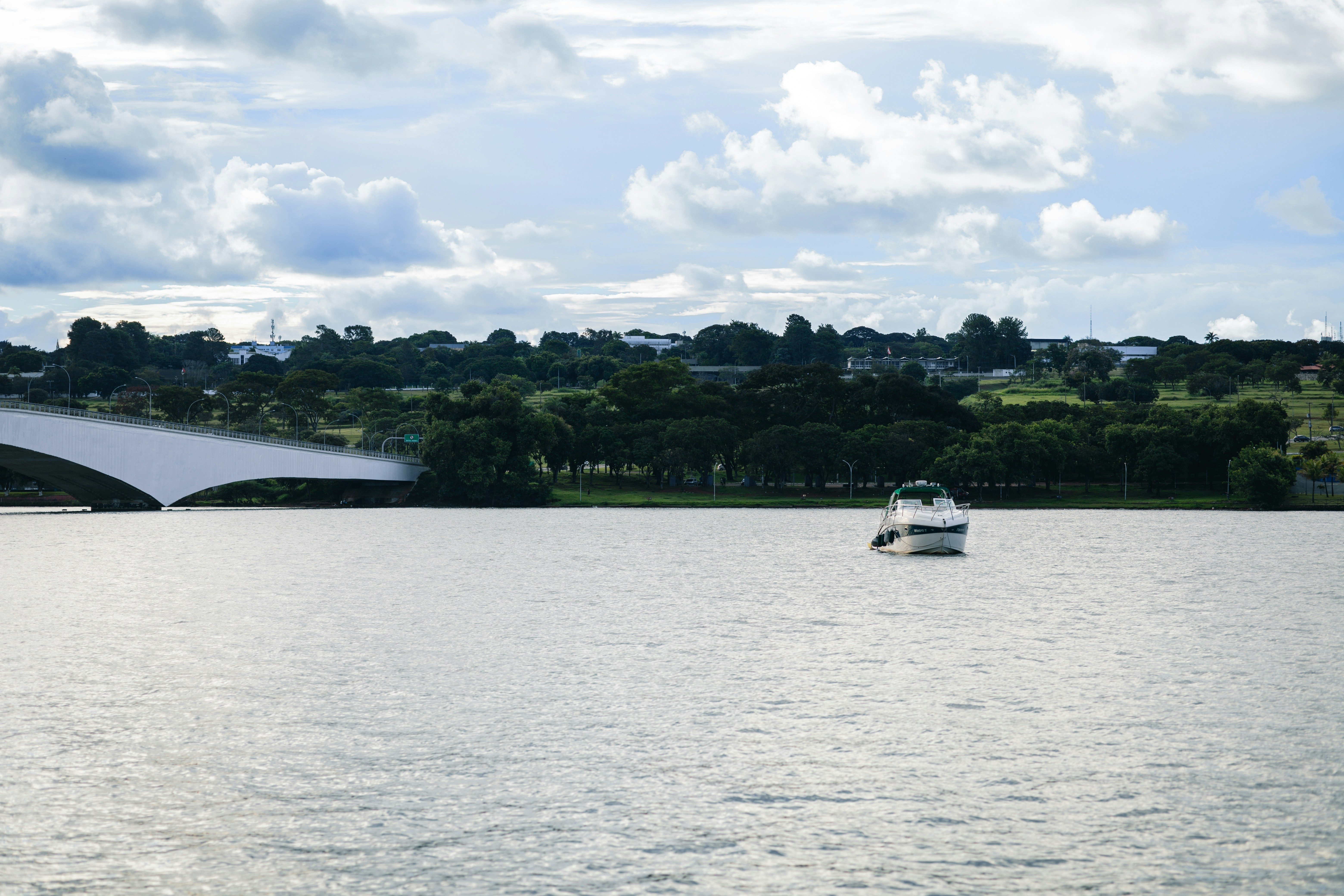 A lone boat glides across a quiet river under a puffy sky
