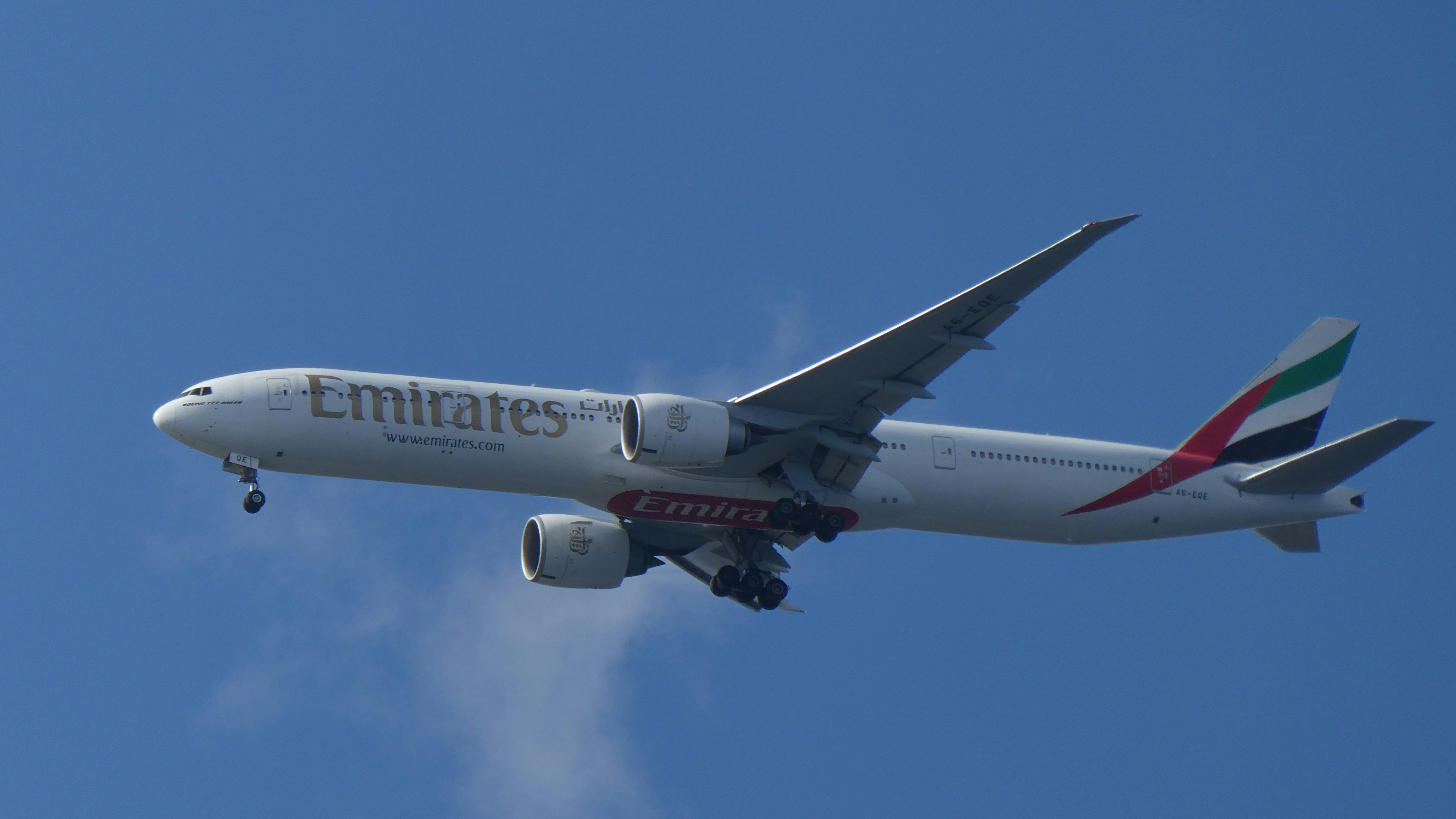 Emirates A380 in ascent: wings, engines, and tail against a clear blue sky