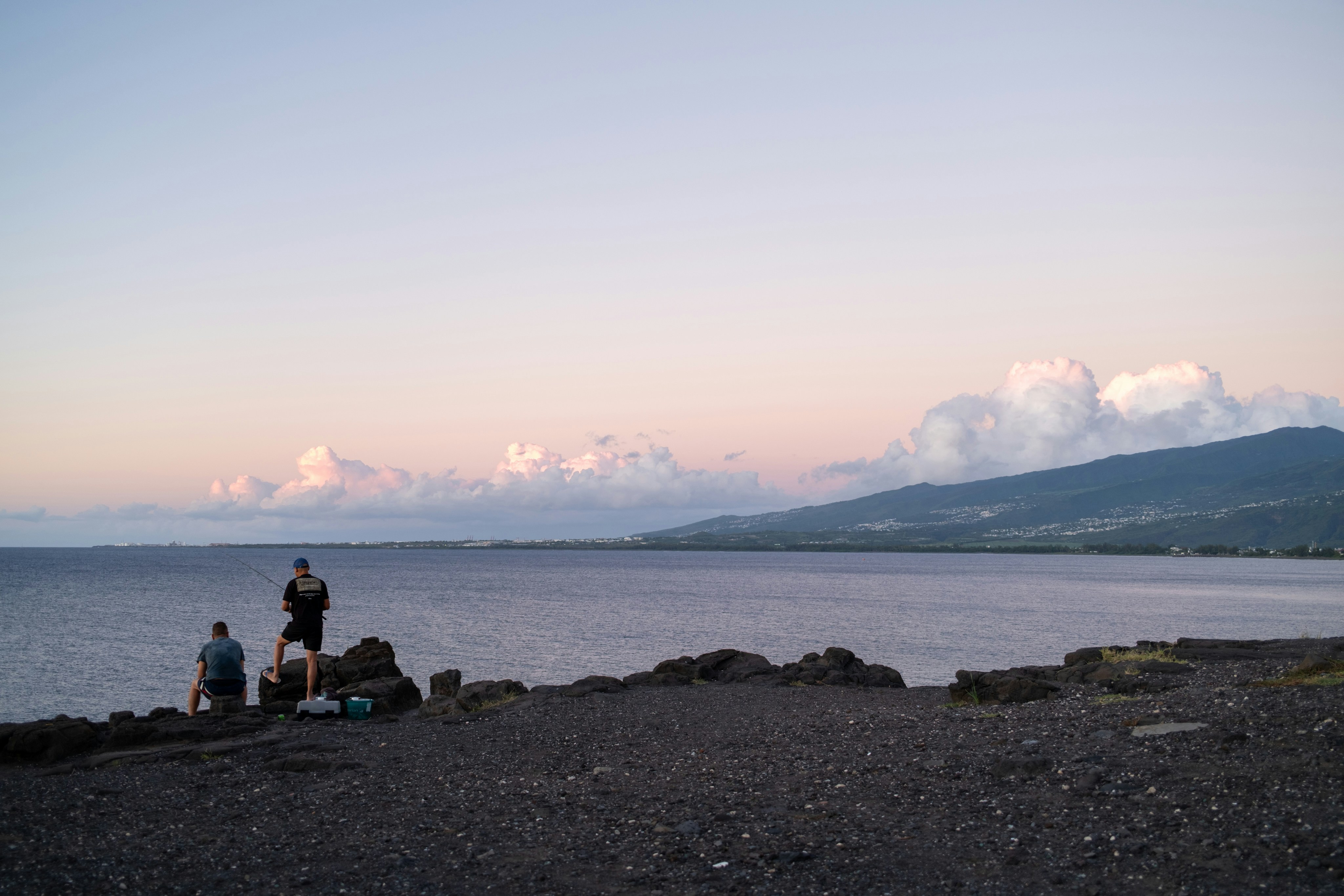Coastal Evening: Two Figures by the Rocky Shore as Distant Hills Glow