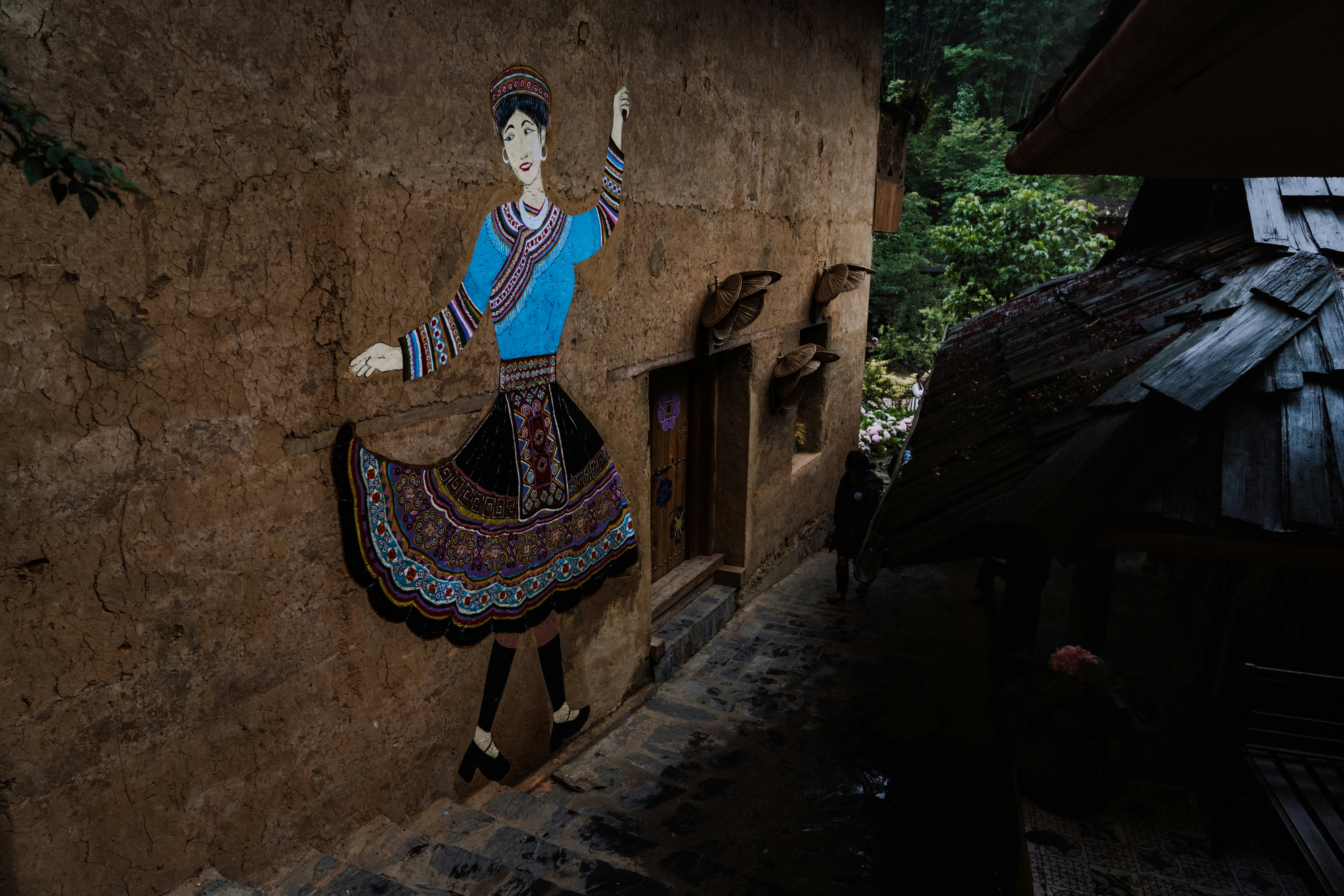 Painted Dancer on Earthen Wall in Narrow Mountain Lane