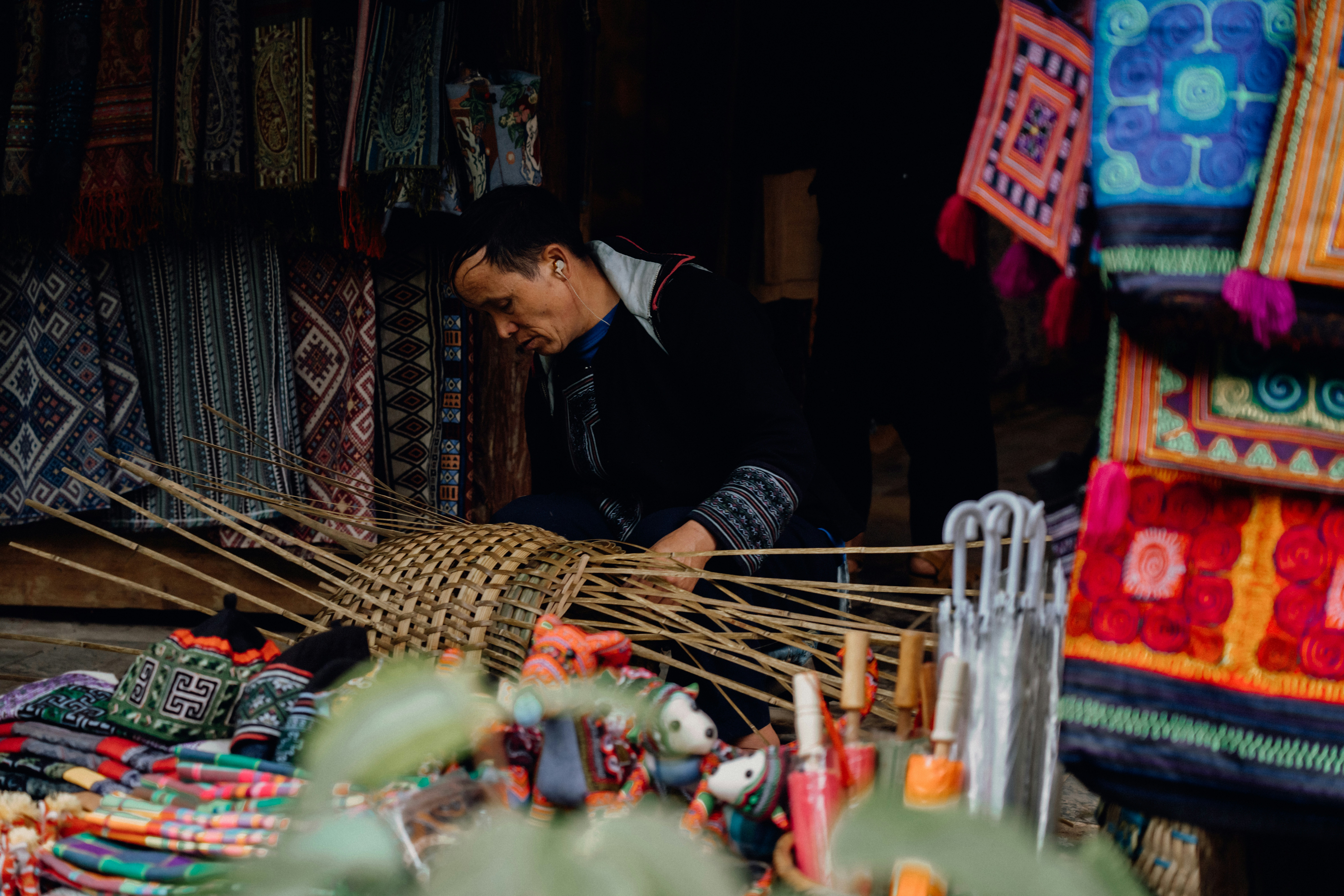 Weaver's Quiet Gaze Amid Colorful Market Textiles