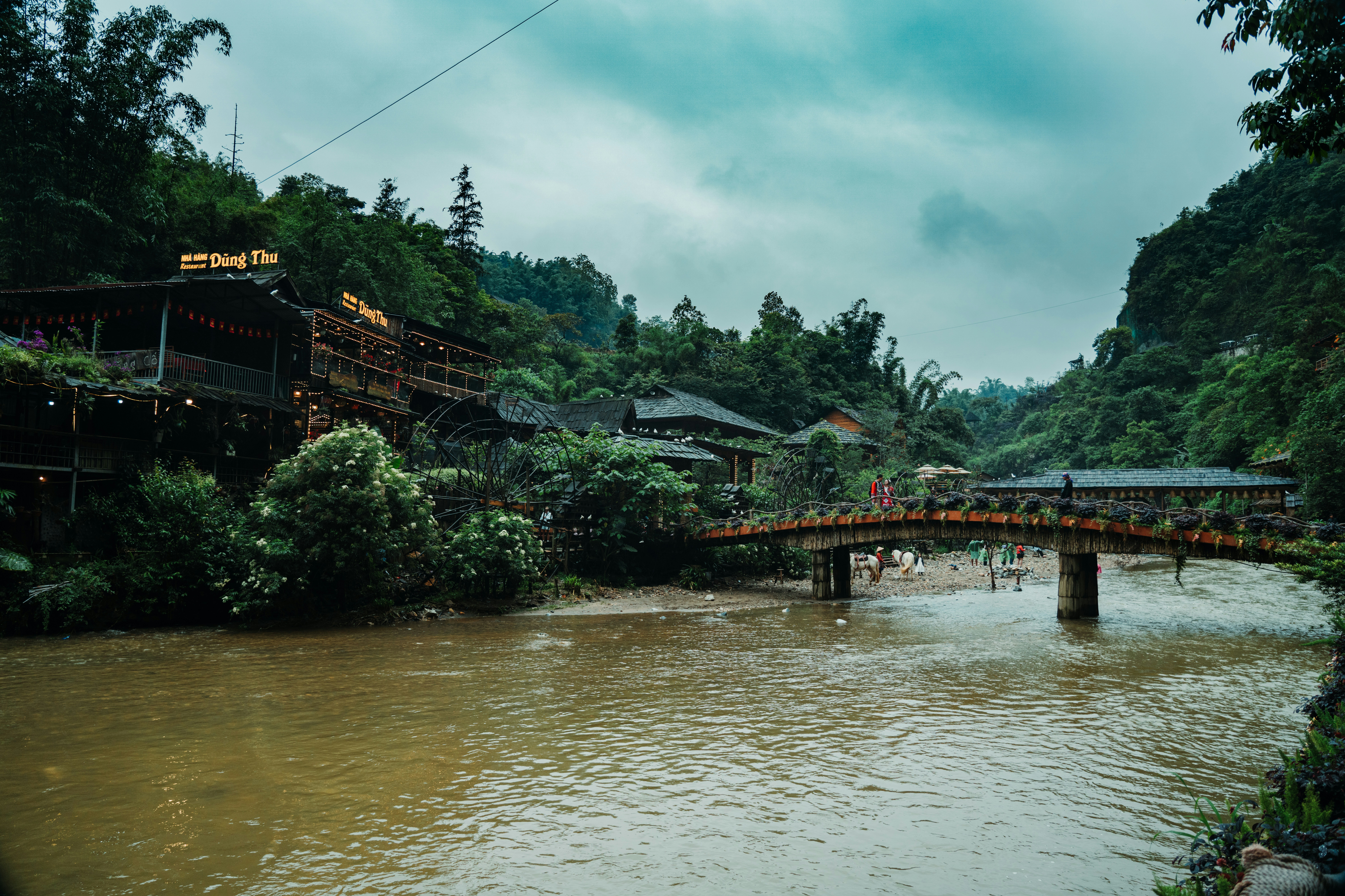 Riverside eateries and arched bridge tucked in a misty hillside village
