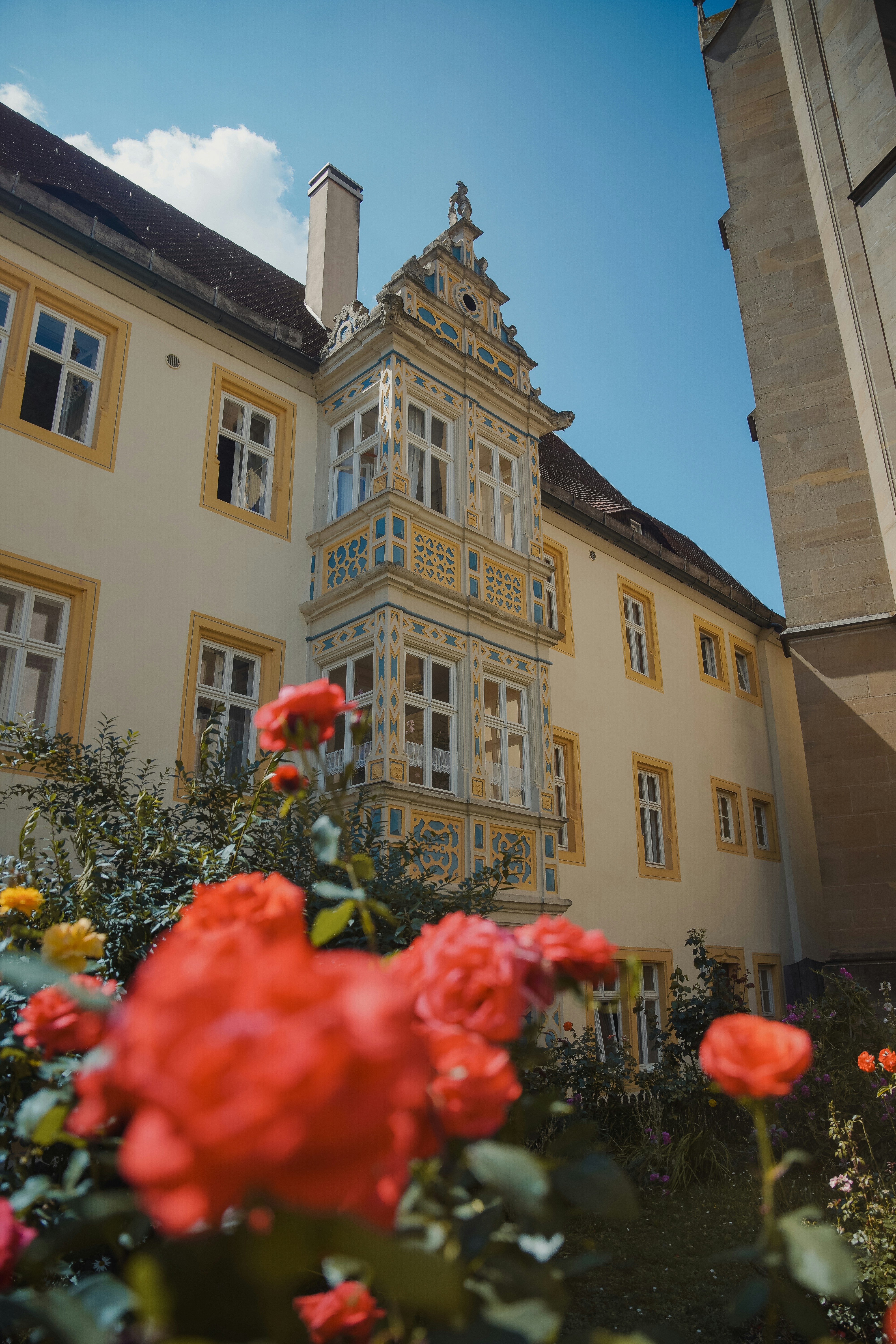 Sunlit Facade with Ornate Balcony Surrounded by Blooming Roses