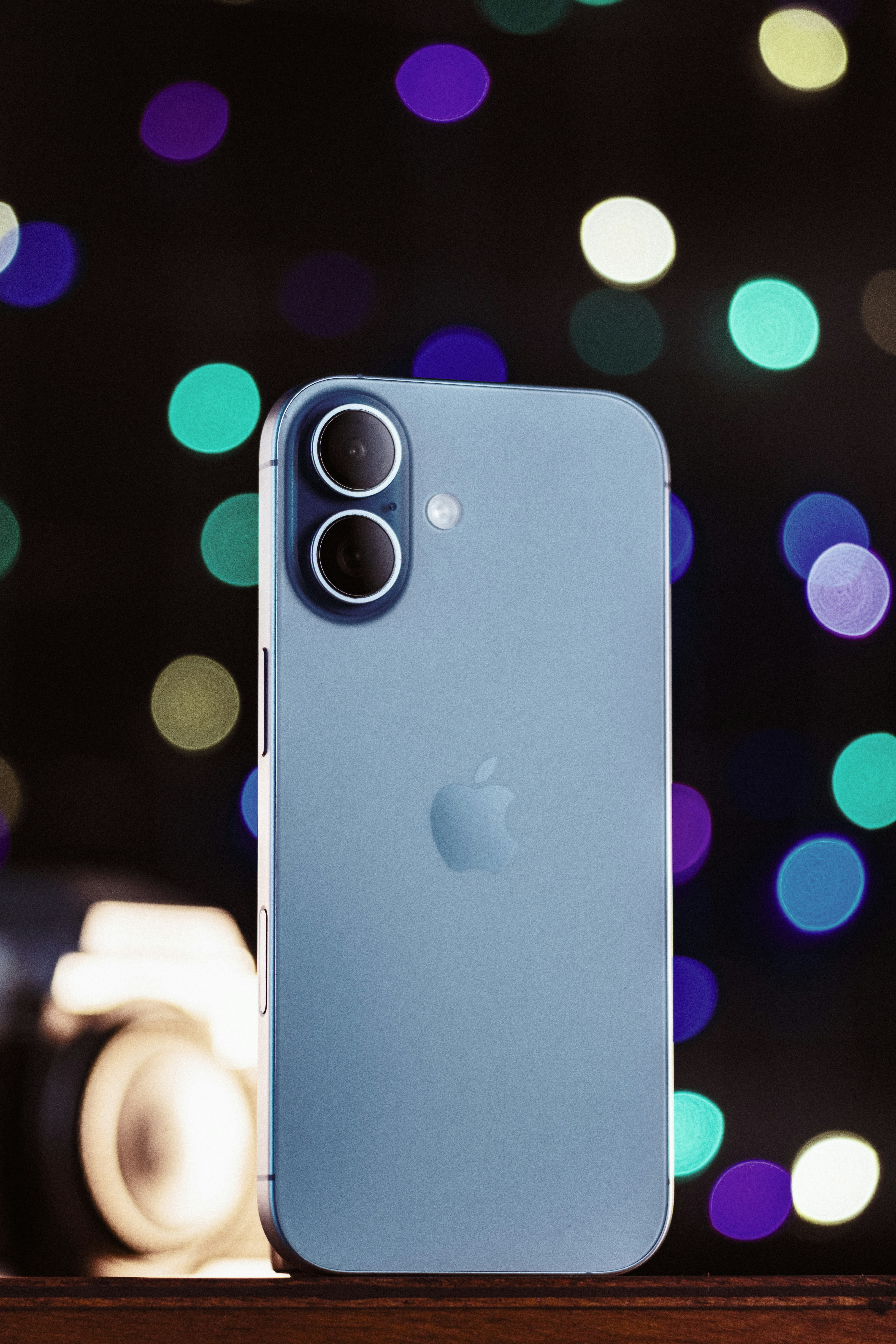 Blue iPhone with dual cameras stands upright against bokeh city lights