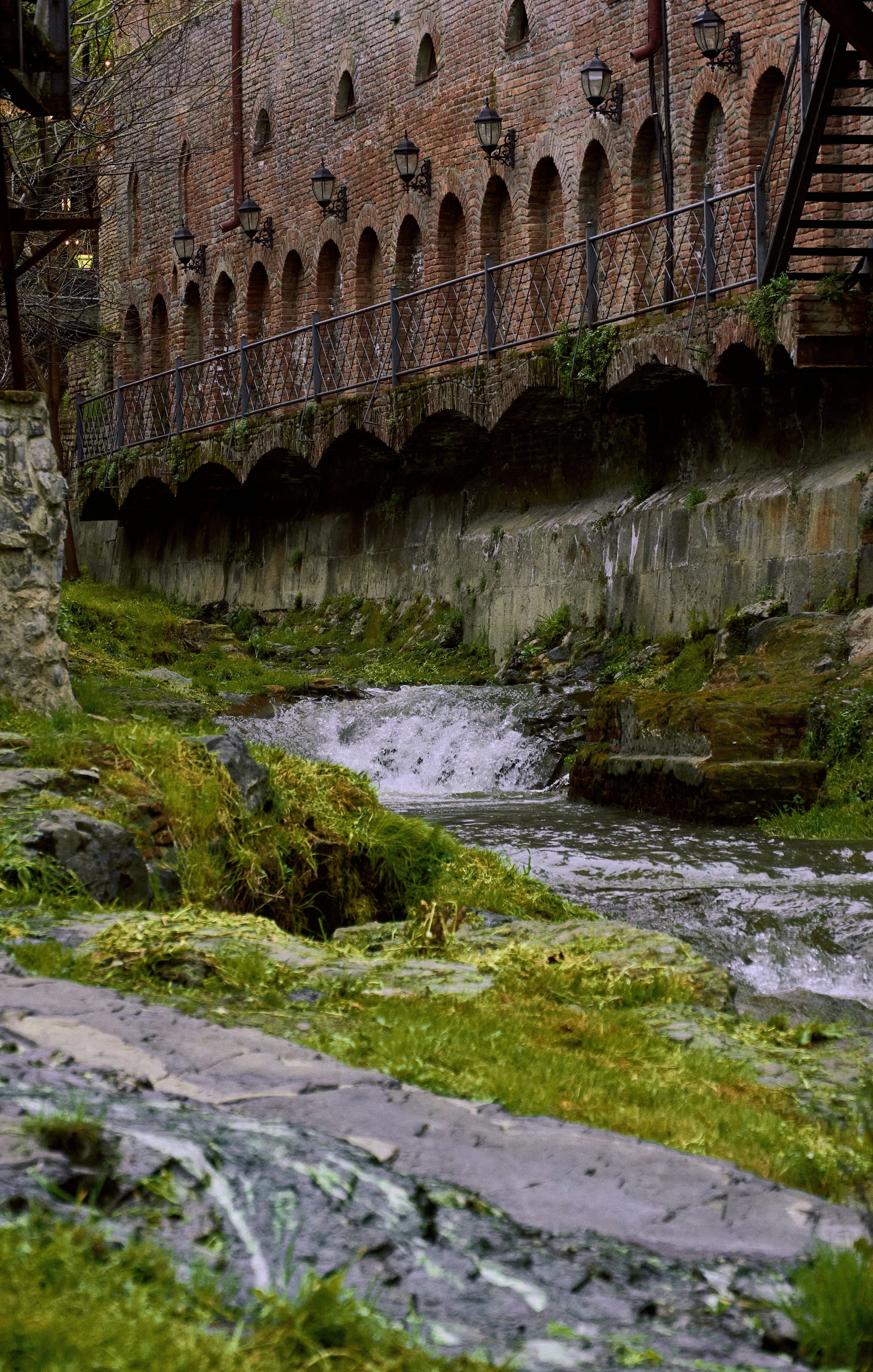 Mossy ruin by a ivy-draped brick bridge over a rushing stream