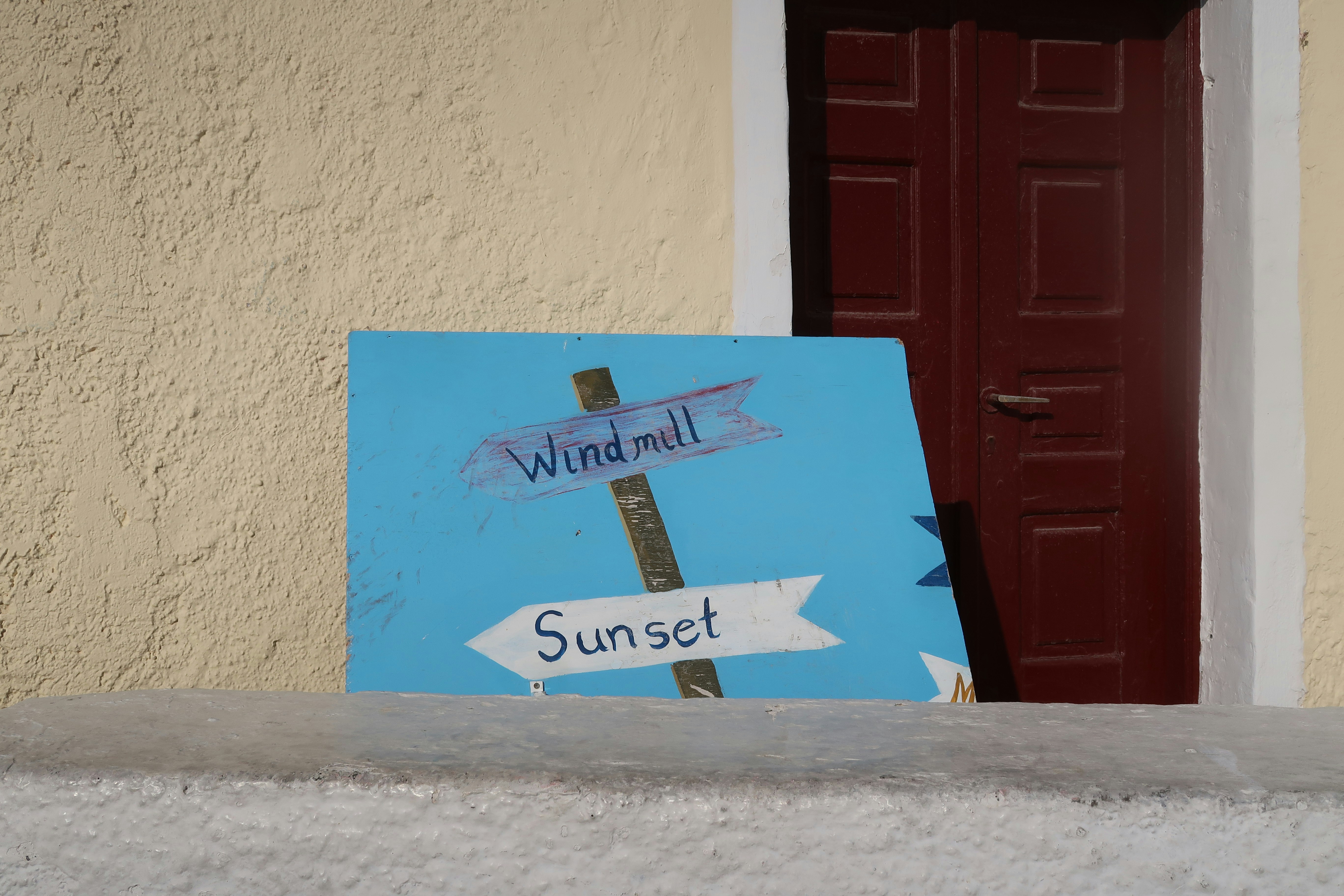 Signpost of Sunsets: Windmill and Sunset Labels Beside a Red Door