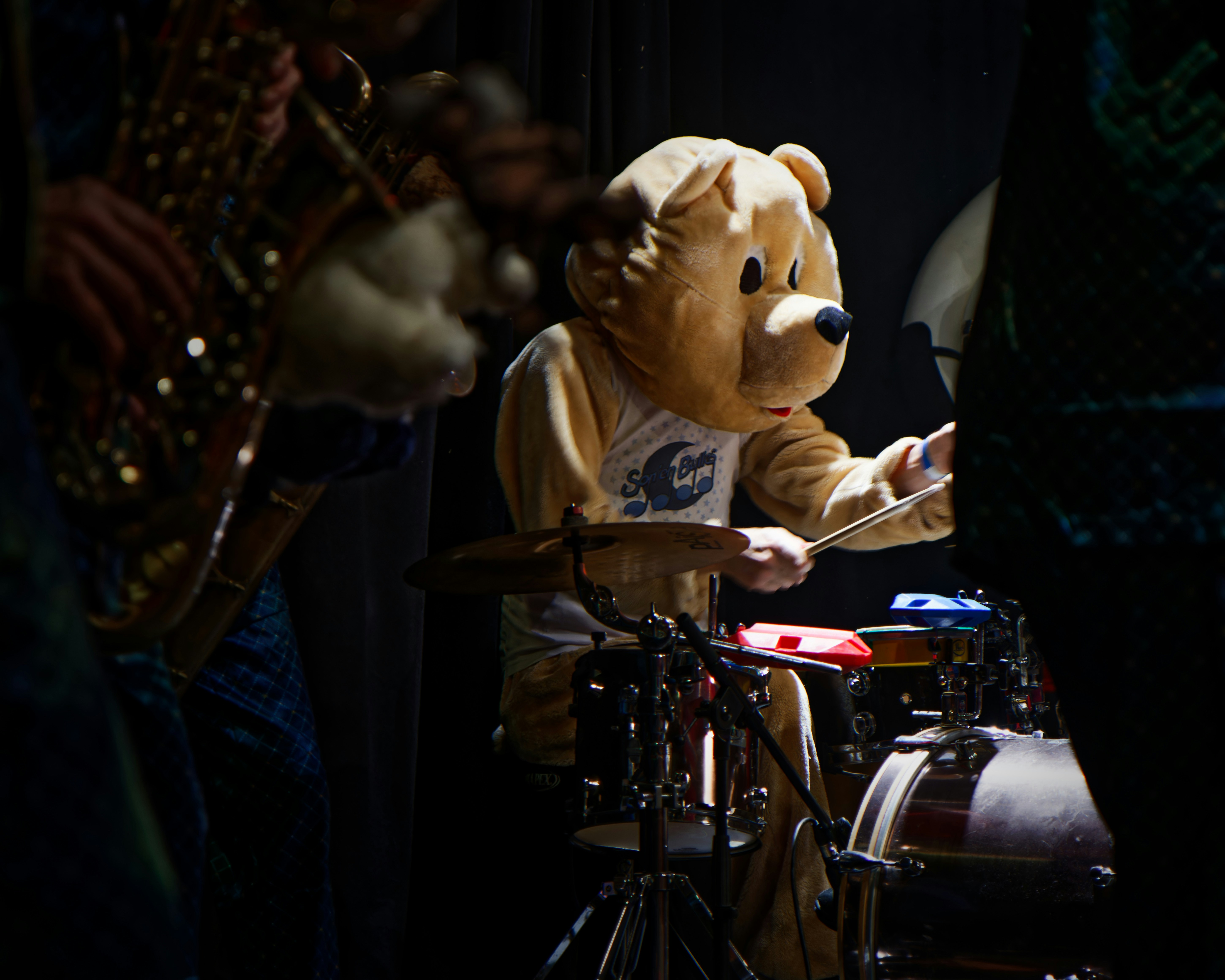 Bear behind the kit: a furry drummer anchors a dim backstage scene