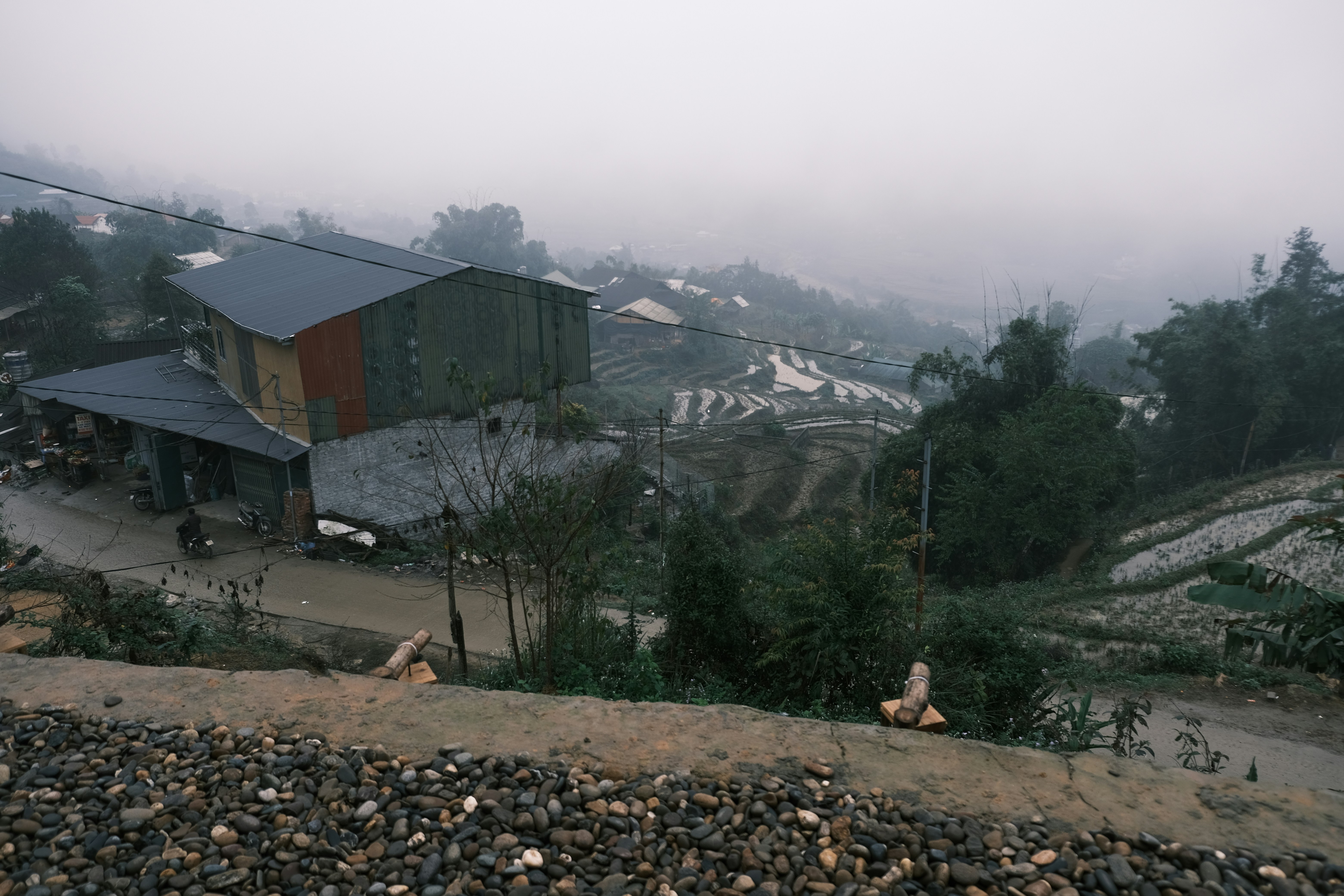 Terraced valley village under mist, framed by a quiet roadside