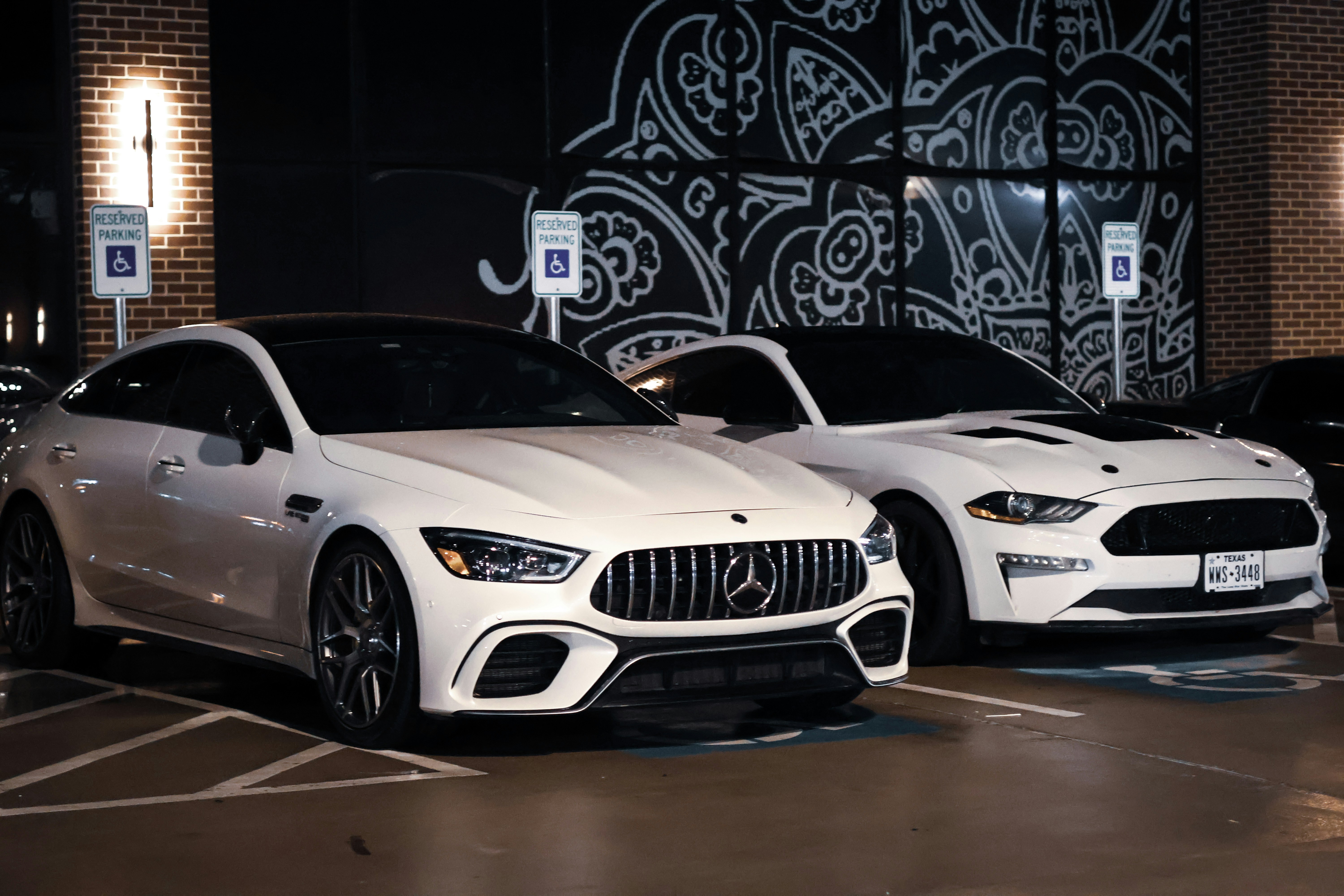 White luxury sedans bask under gallery lighting in a dim lot