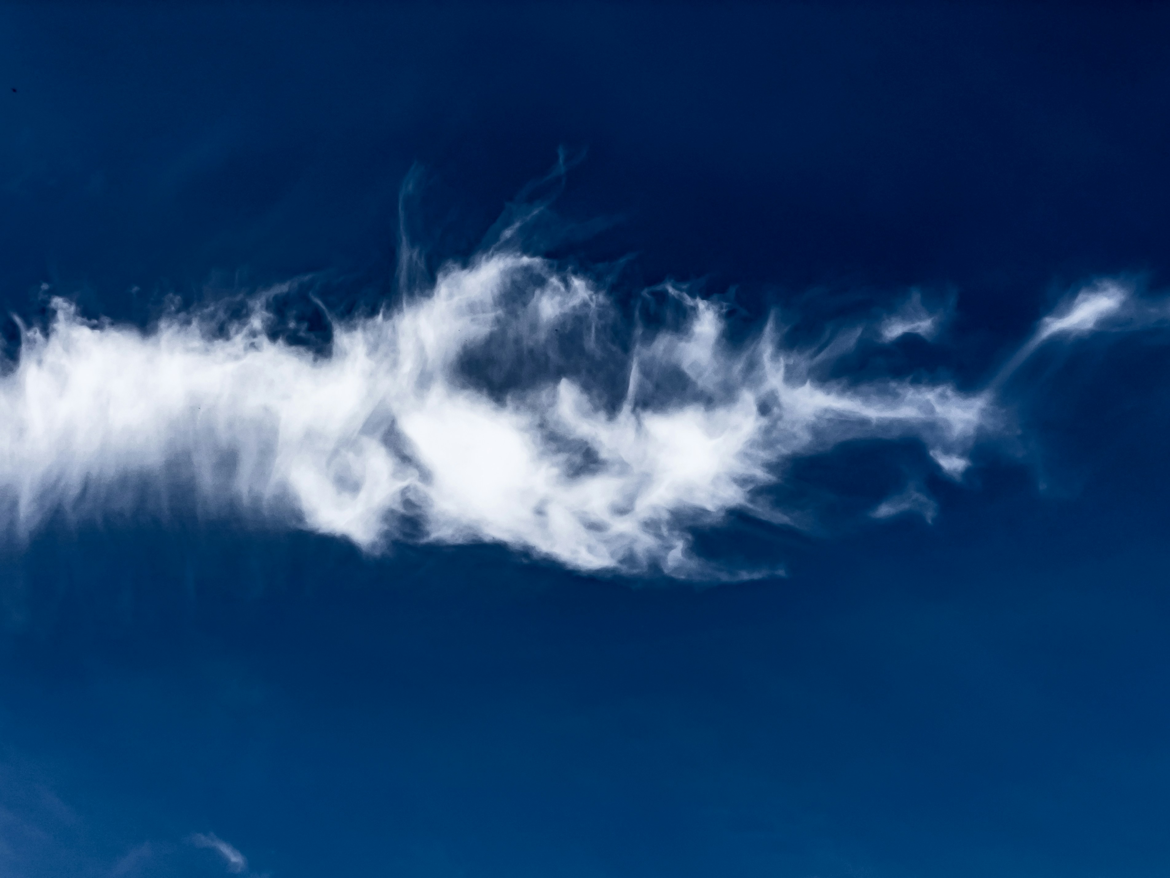 A solitary wispy cloud drift across a deep blue expanse