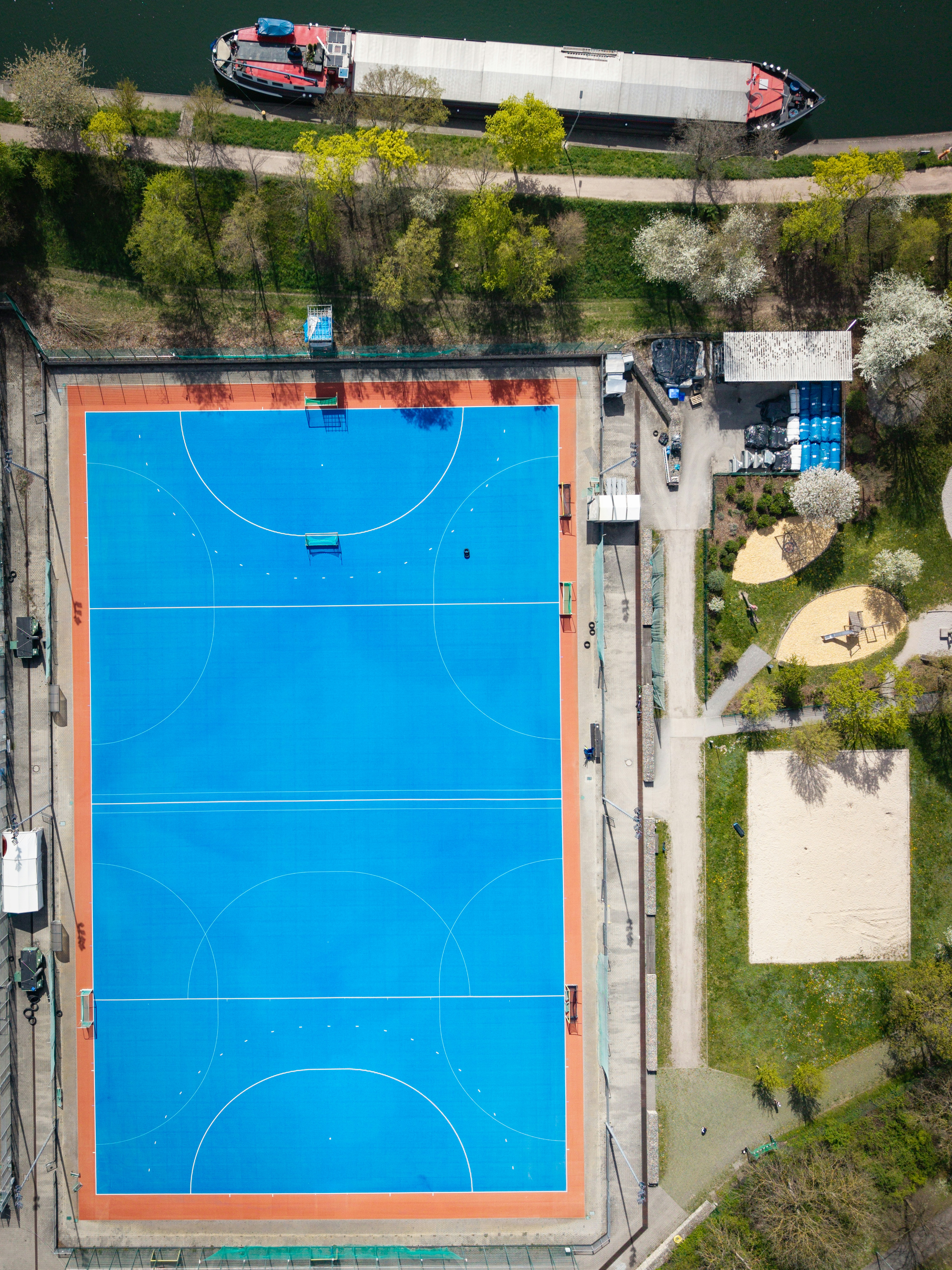 Aerial View of a Bright Blue Basketball Court Beside a Canal and Green Park