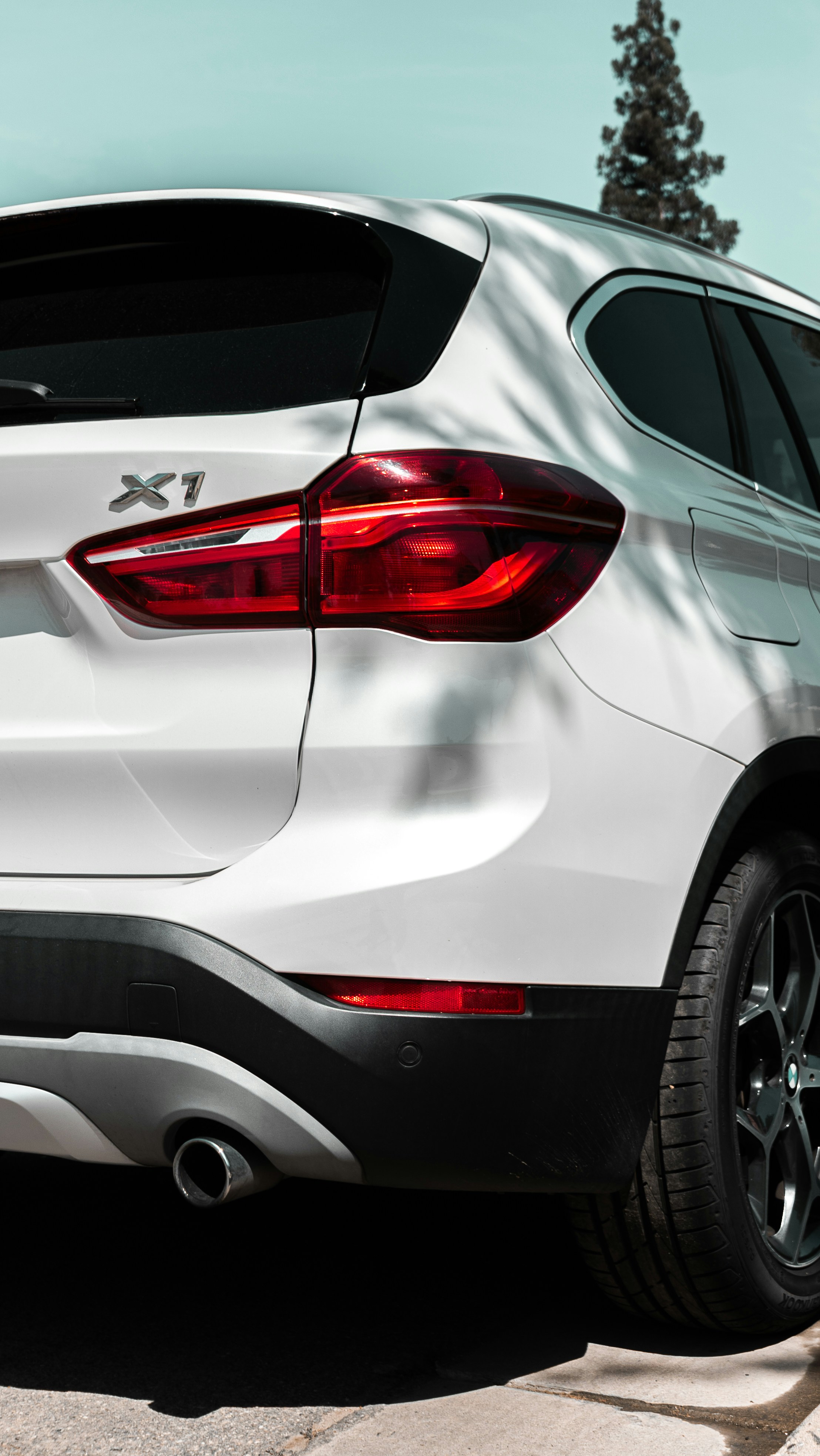 X1 Stance: The rear-quarter of a white SUV under sunlit chrome and shadow