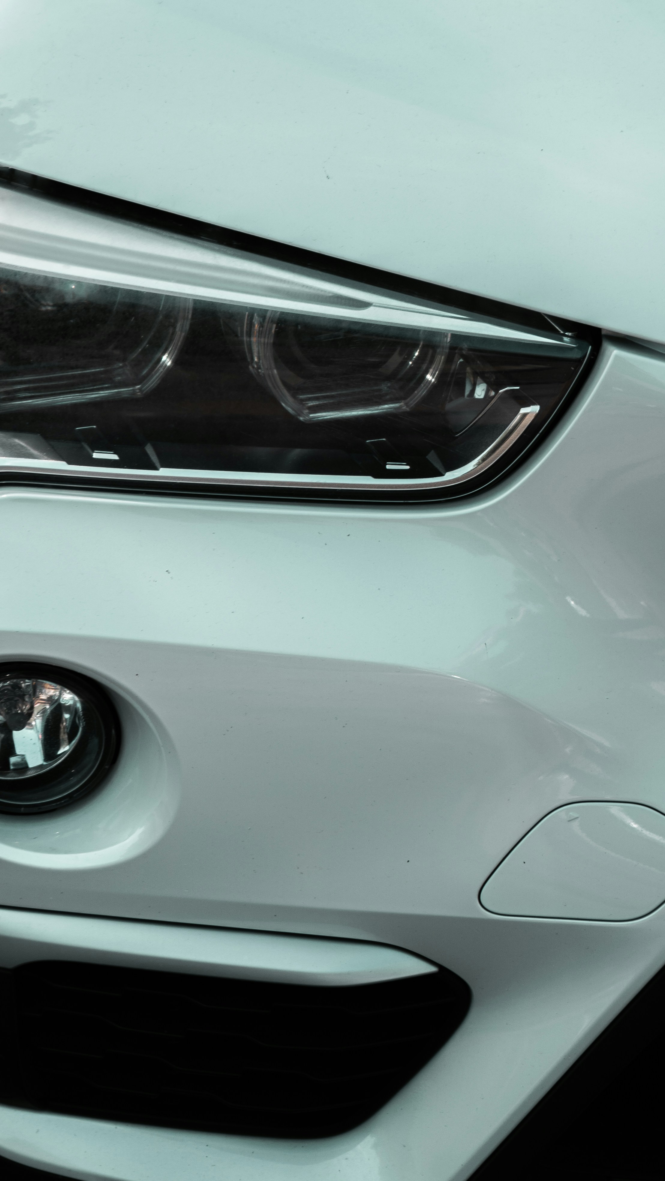 Close-up of a pale front-end: headlight detailing and sculpted bumper on a white car