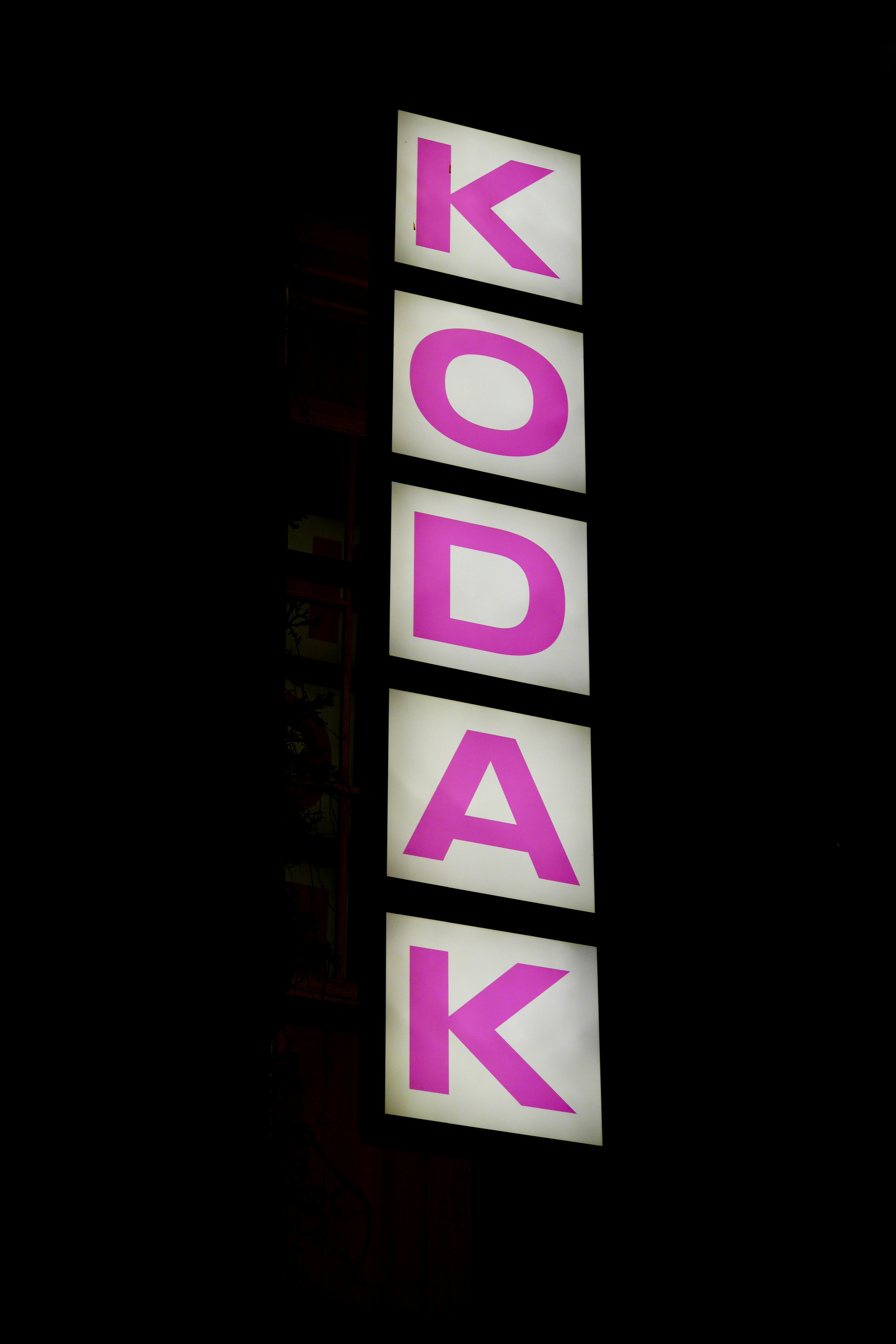 Neon Sign vertically spelling KODAK in magenta against night sky