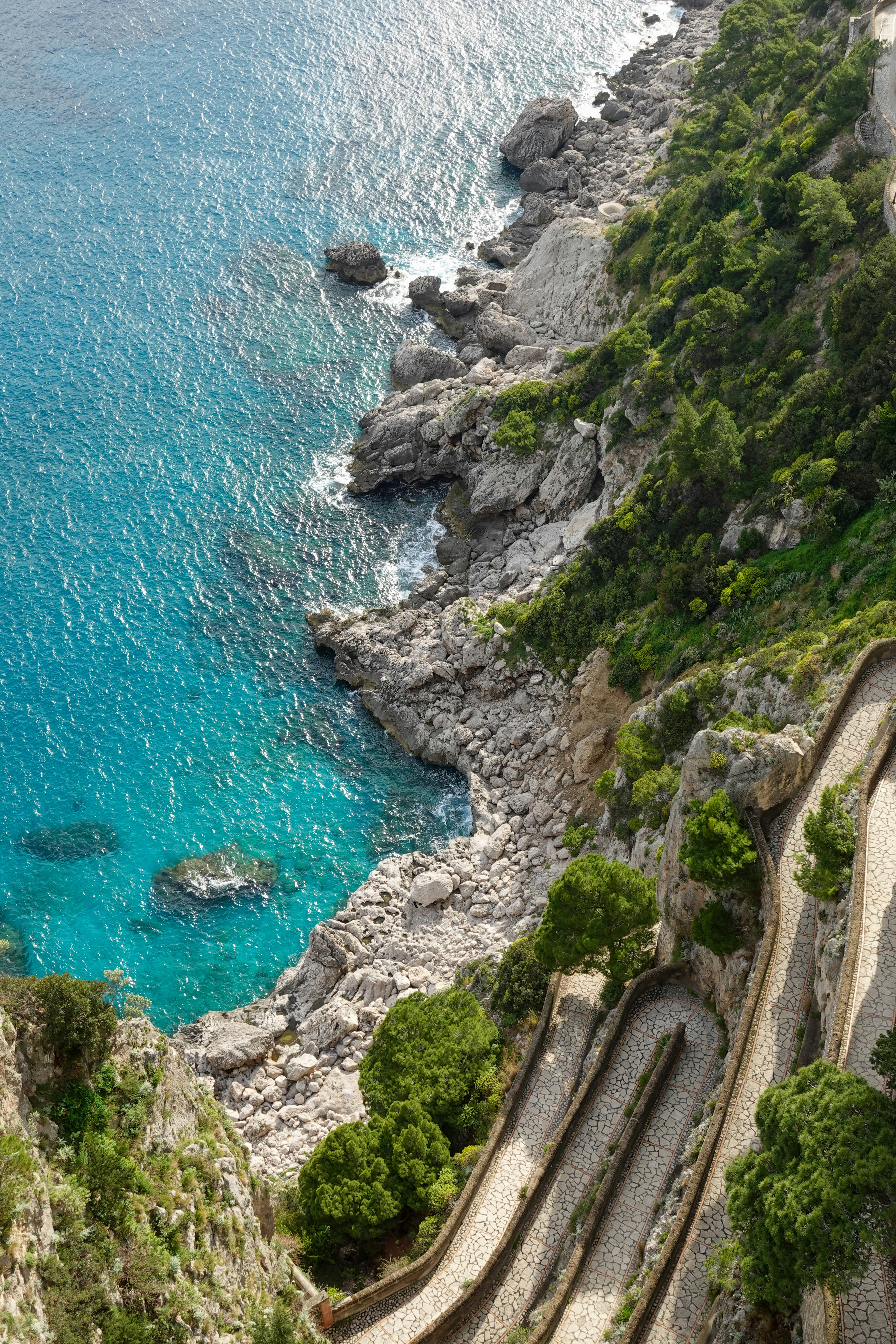Rugged coastal switchbacks wind along sunlit cliffs above turquoise waters