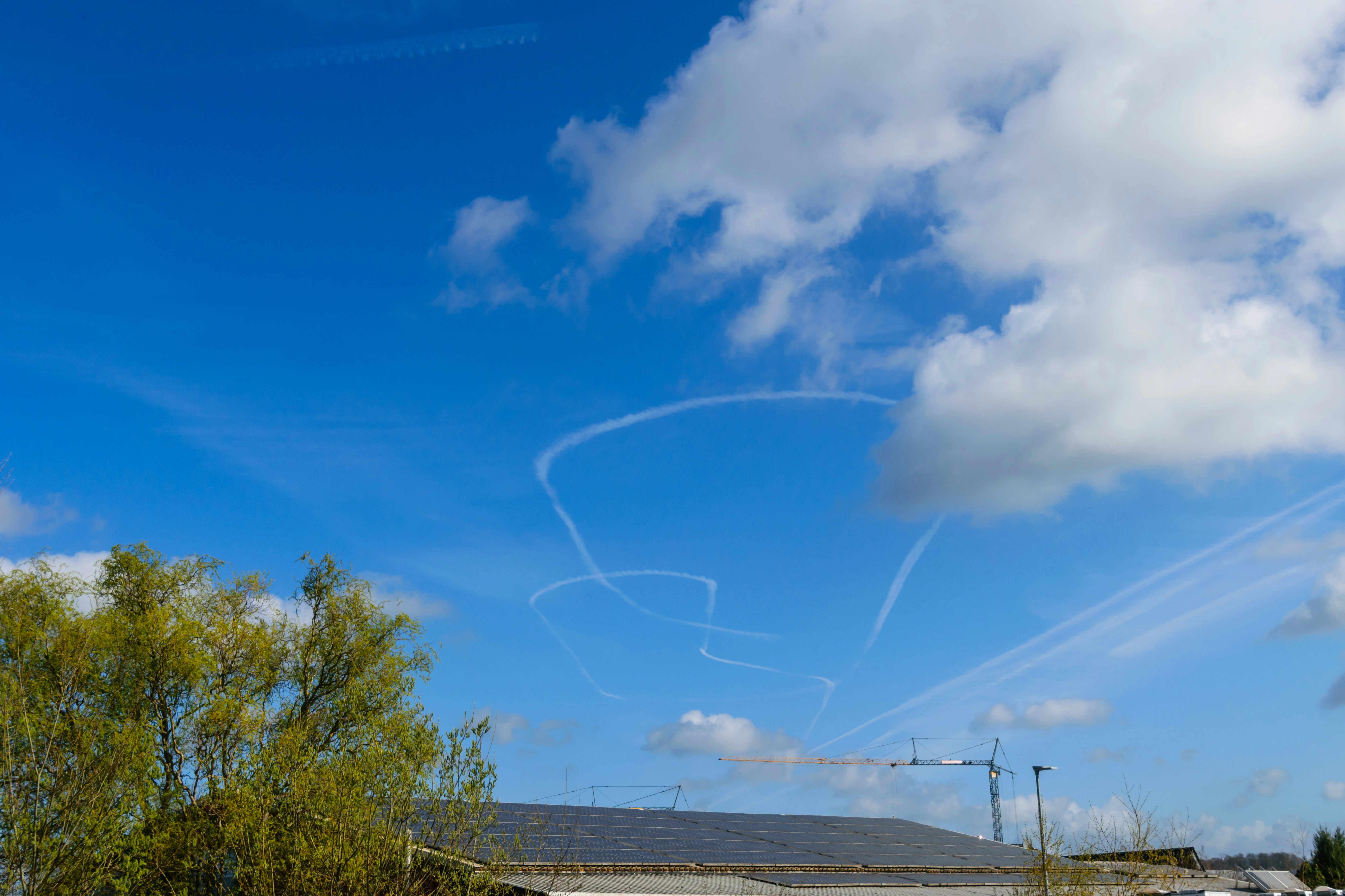 Clear blue sky over a suburban roof with looping contrails