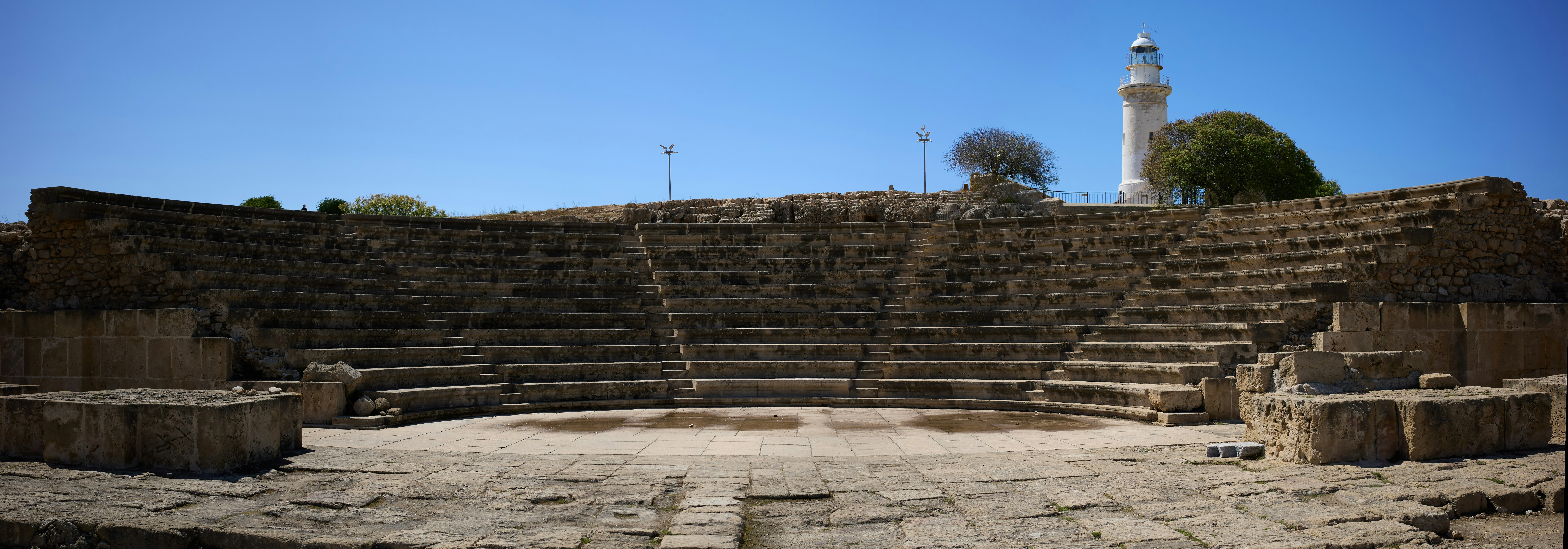 Stone Auditorium Under a Blue Dome: Ancient Theatre Steps and Lighthouse