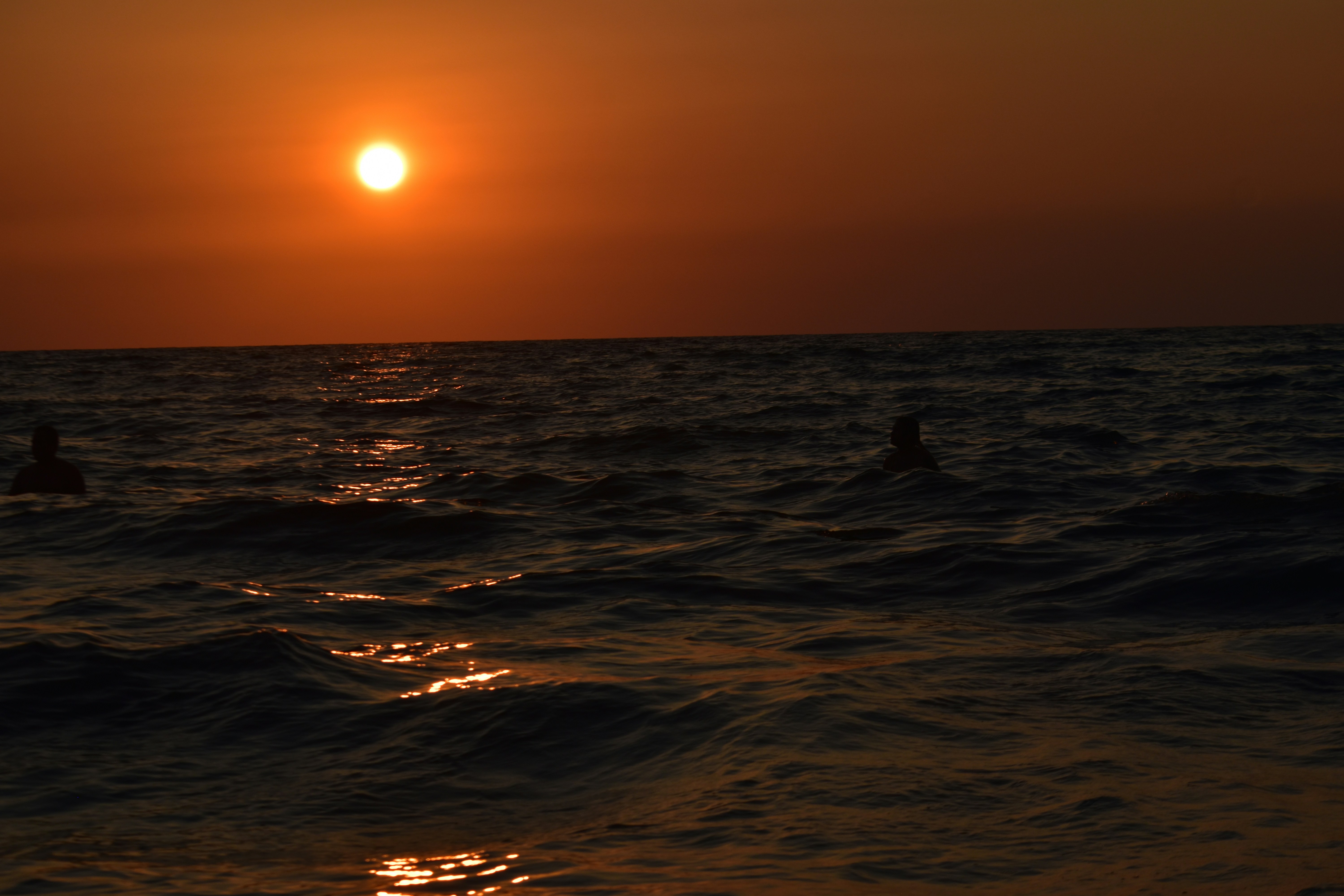 Horizon Glow: Sunset Over Quiet Ocean with Distant Silhouettes