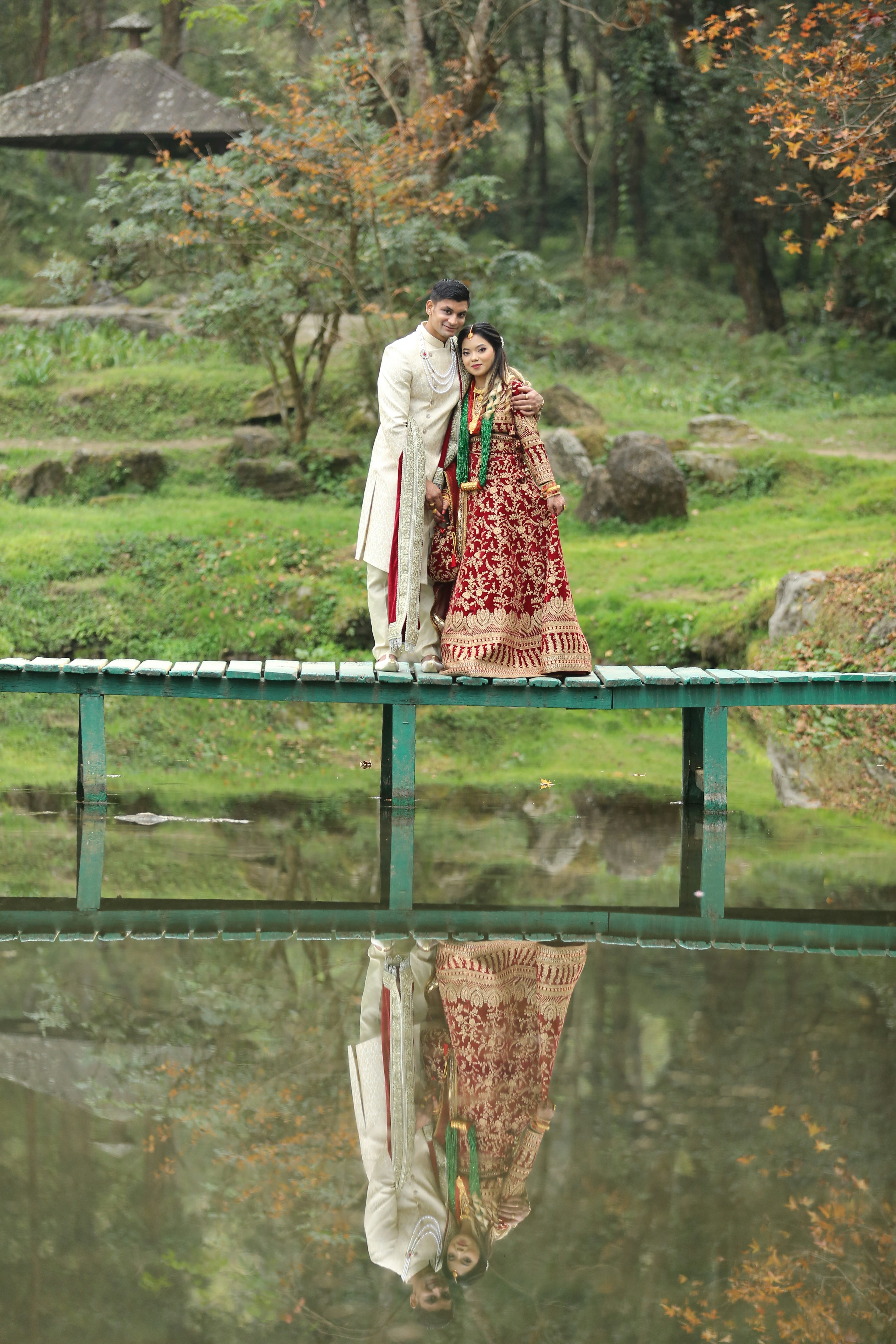 Couple in Traditional Attire on a Serene Park Bridge