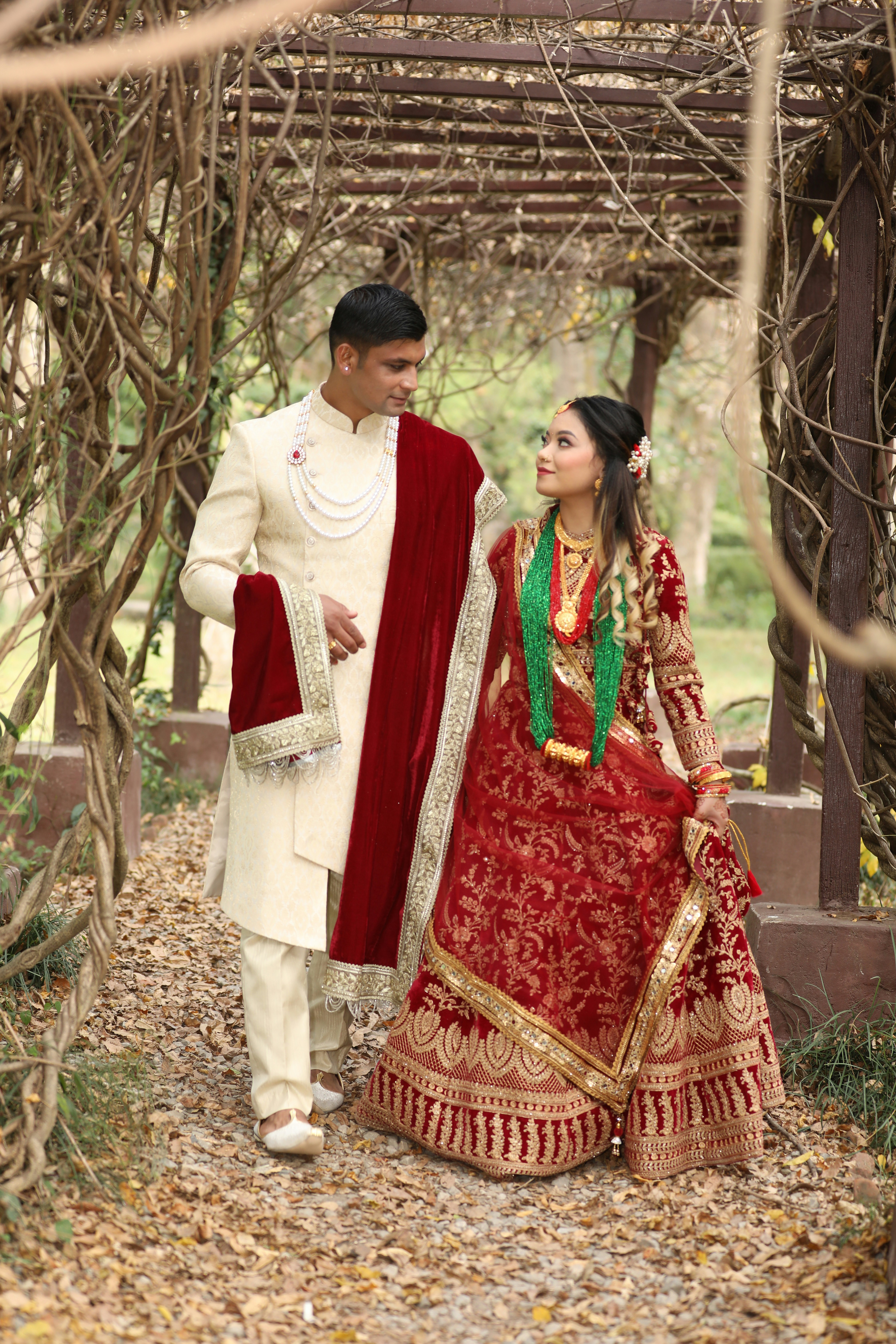 Couple in ceremonial attire strolling under a vine-framed arch