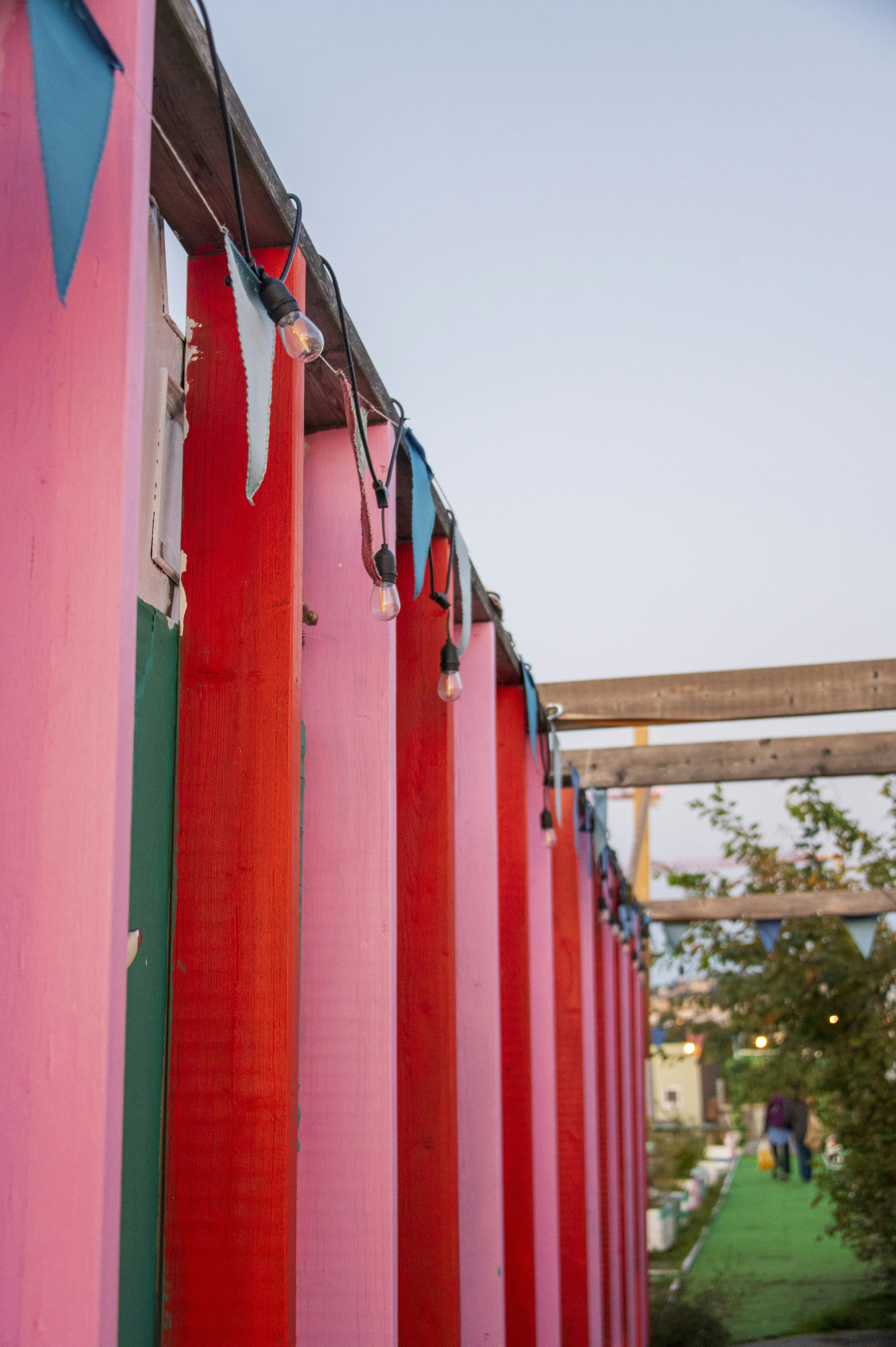 Colorful fence lines and hanging bulbs lead toward a sunlit courtyard