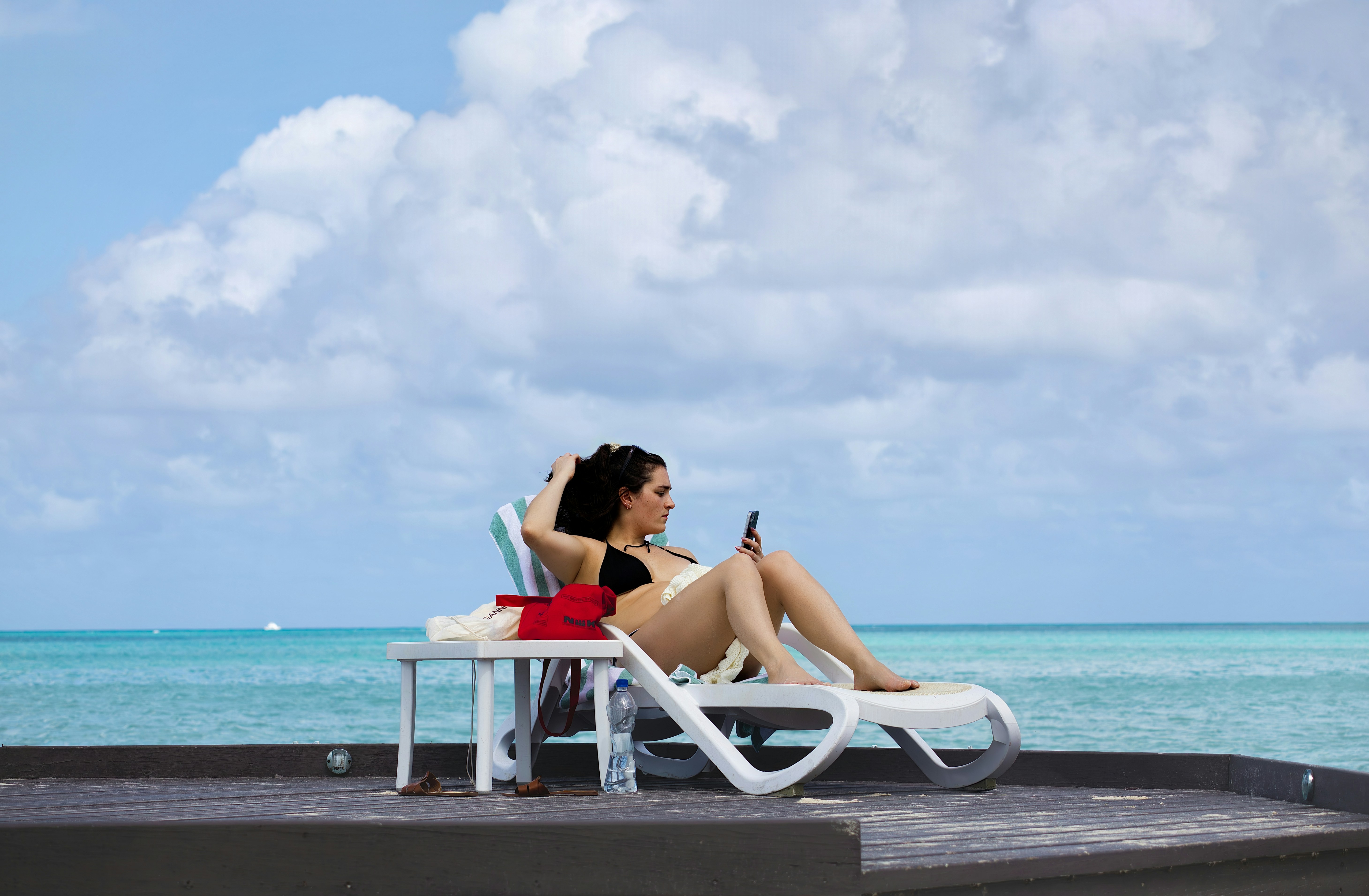 Sunlit Solace: a woman reclining on a white lounge by turquoise seas