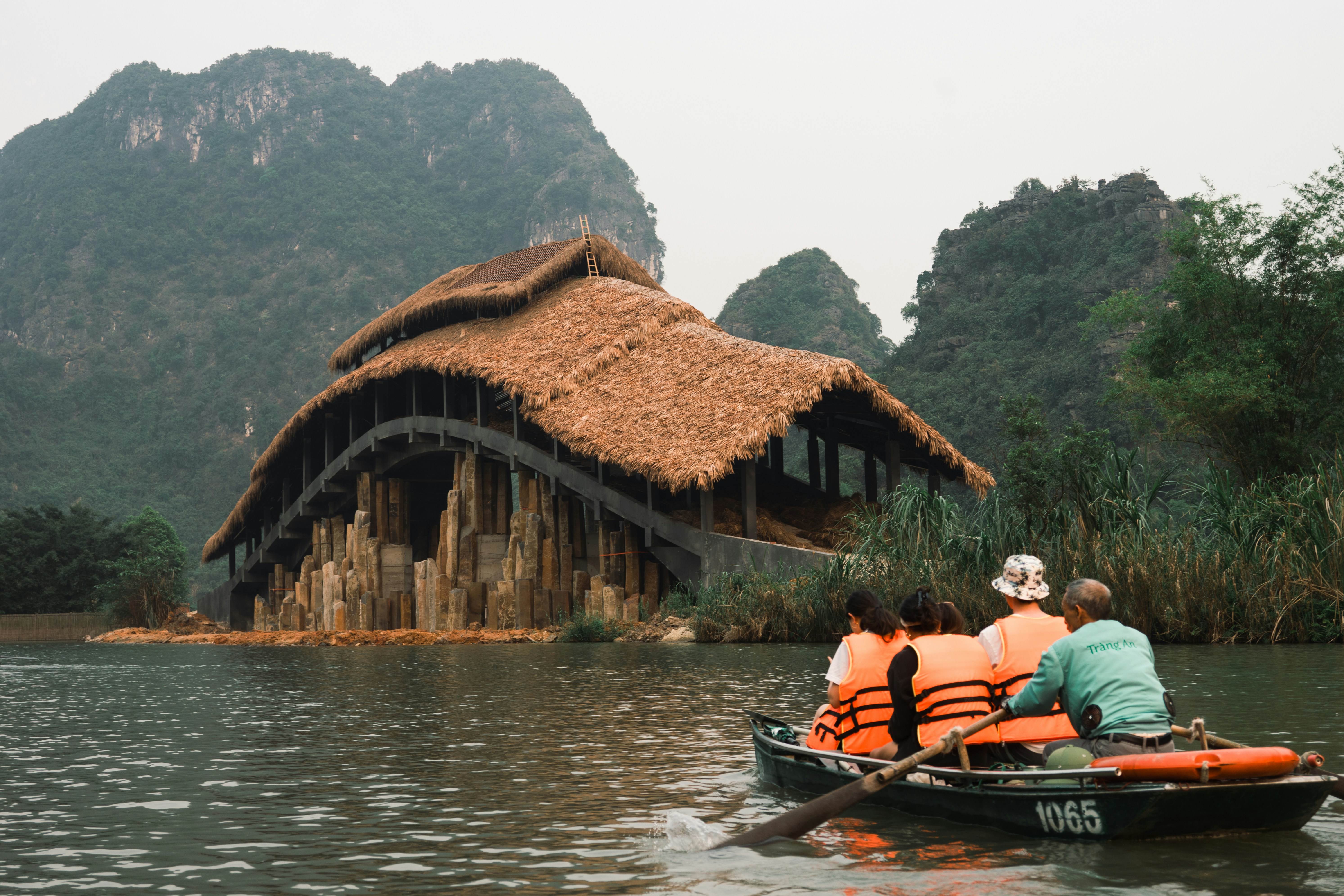 Whispering thatched-roof hut gliding past a bamboo-arched lake