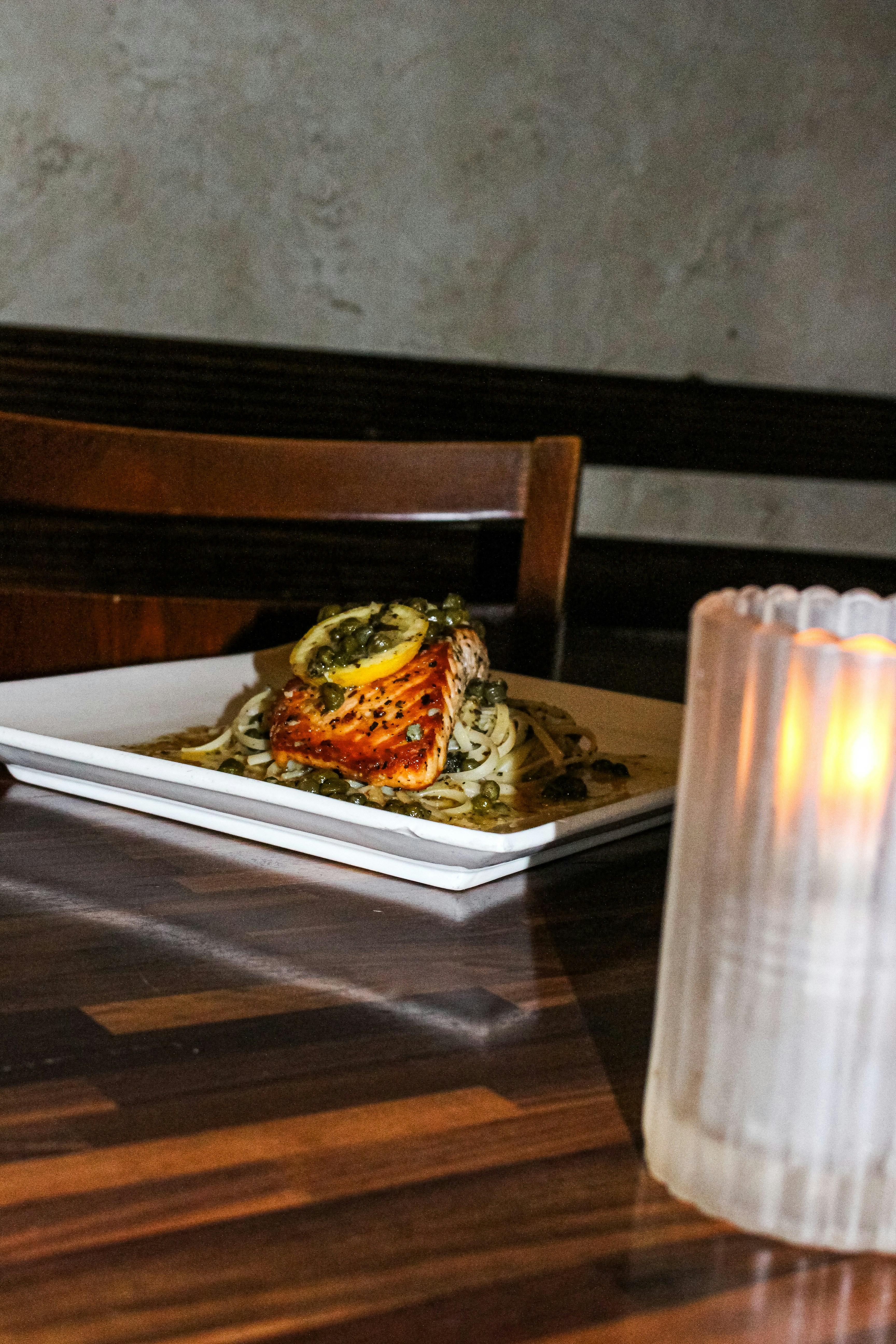 Seared Salmon on herb-laced pasta, softly lit by a glowing table candle