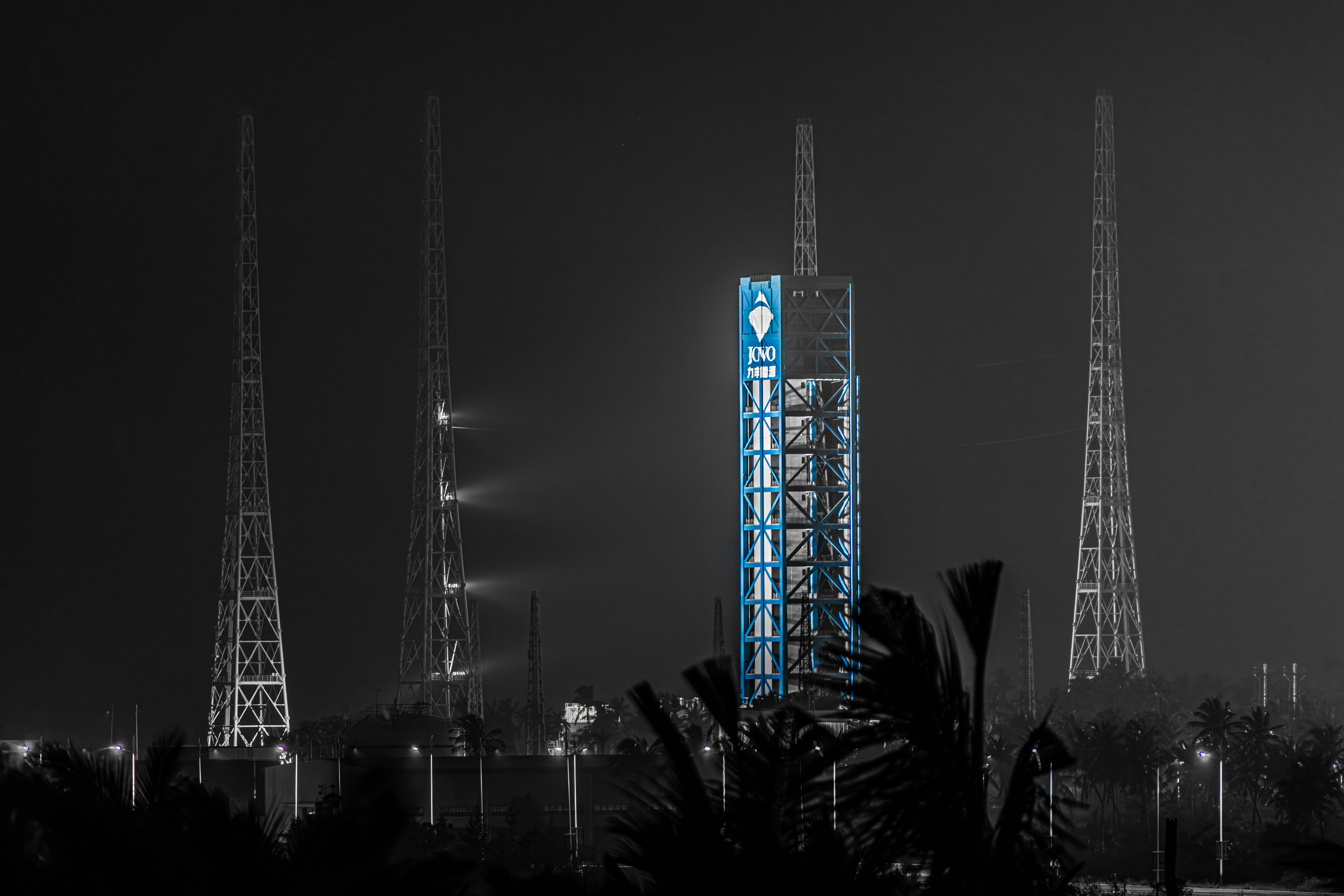 Blue-clad launch tower silouetted at night among skeletal masts