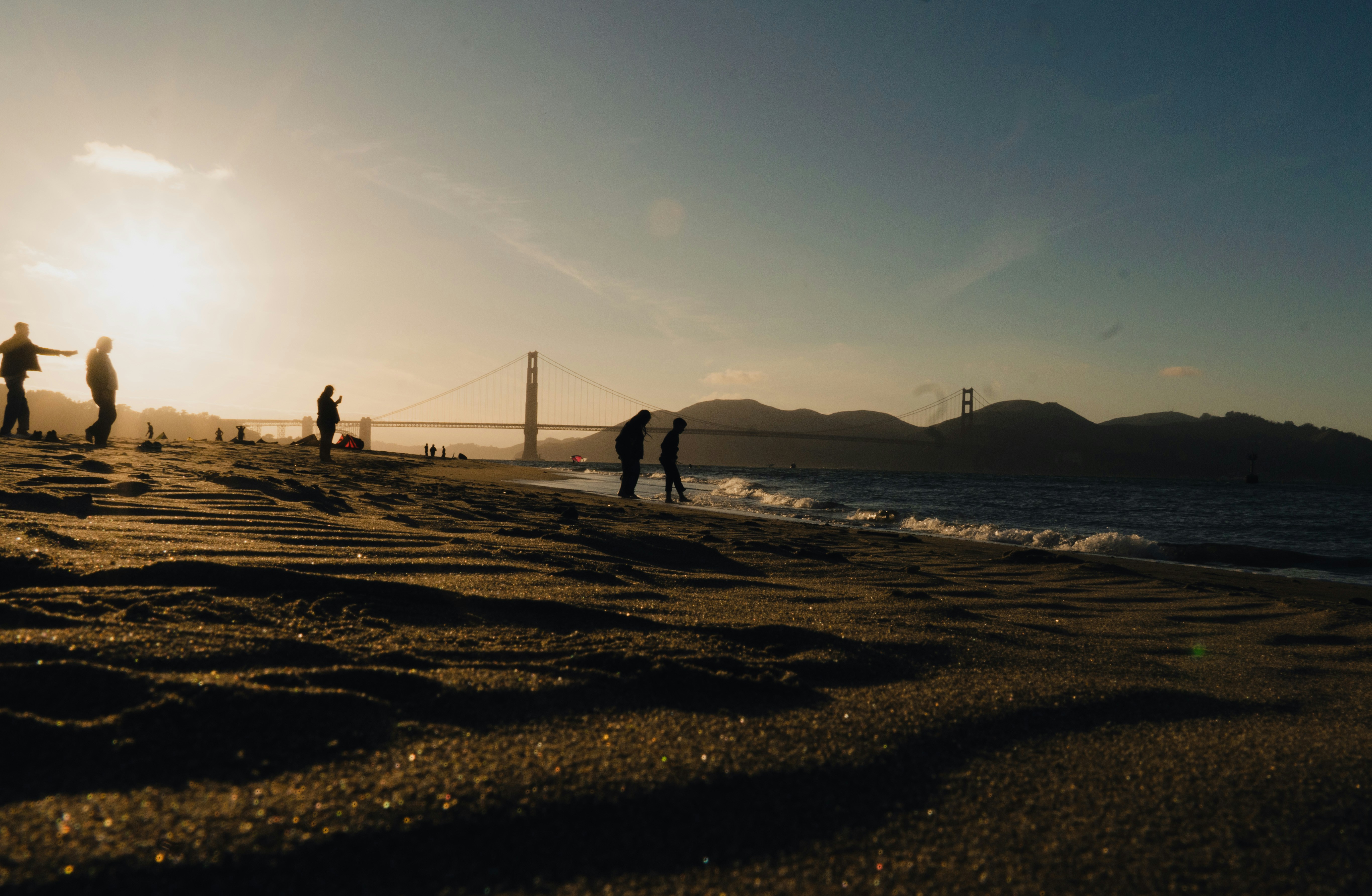 Golden Hour Stroll: Silhouettes on a Sunlit Shore with the Golden Gate Bridge in the Distance