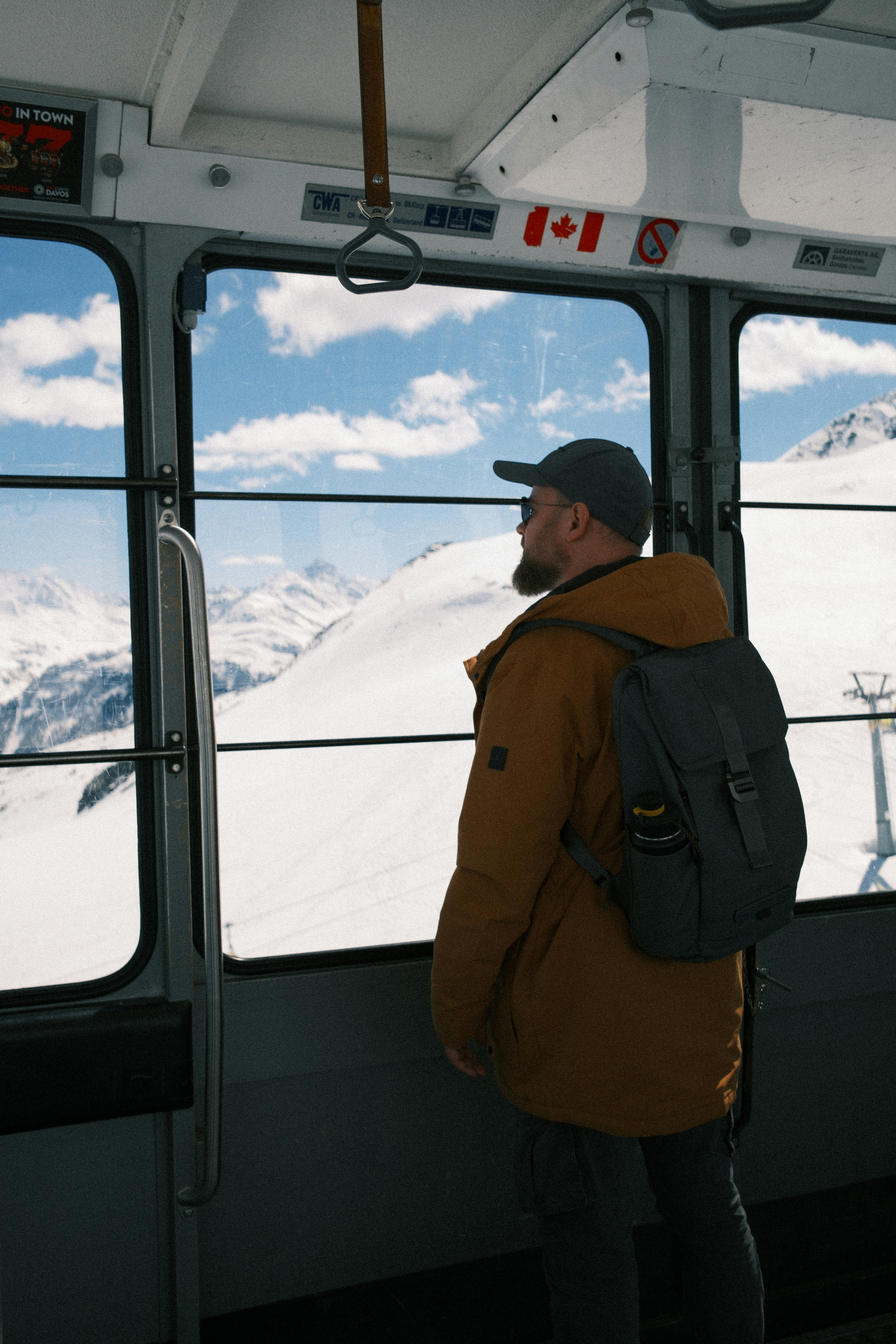 Mountaintop Commute: A Backpacked Traveler Gazes at Snowbound Peaks from a Cable Car