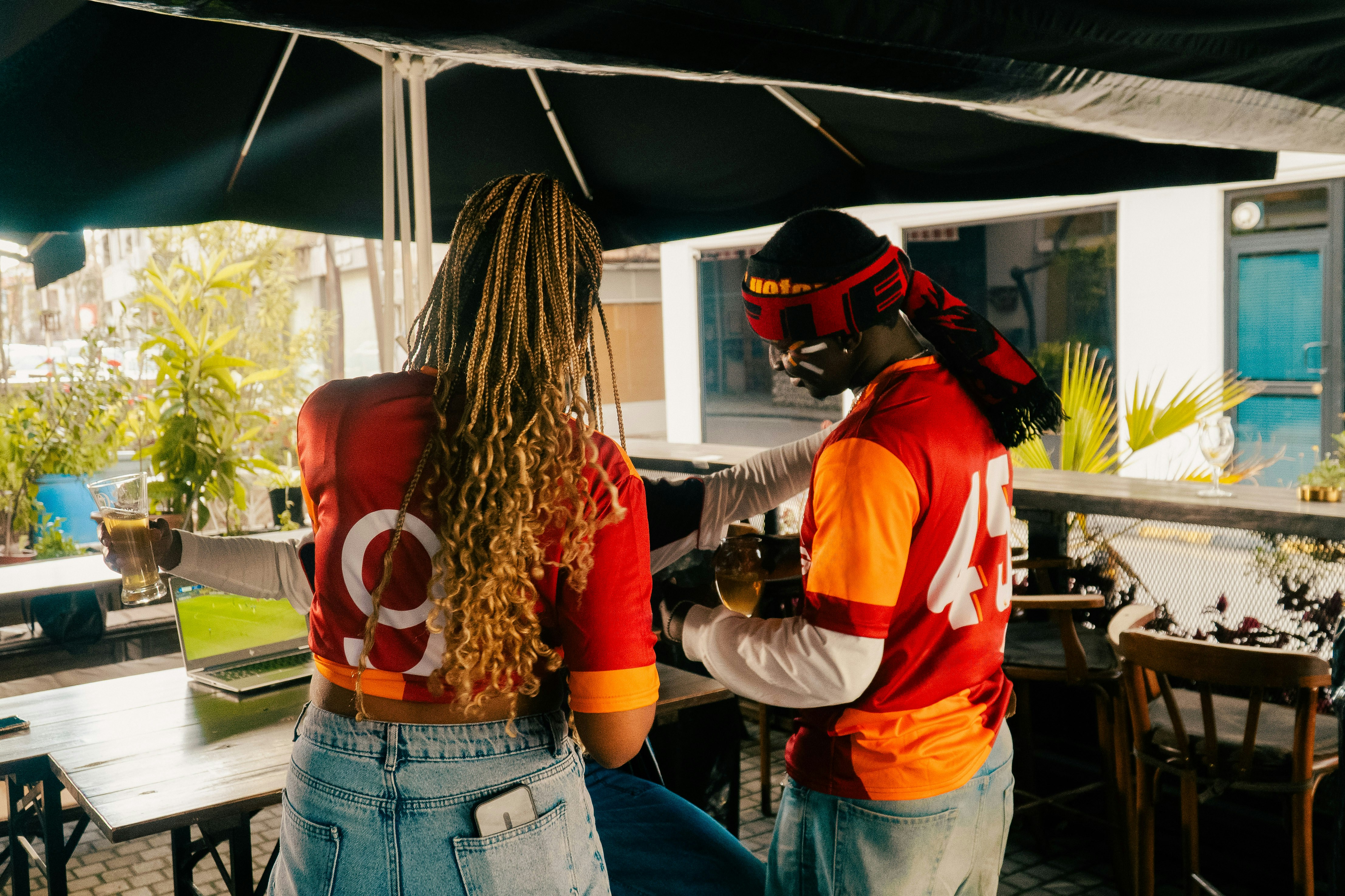 Two Football Fans in Colorful Jerseys Under an Outdoor Canopy