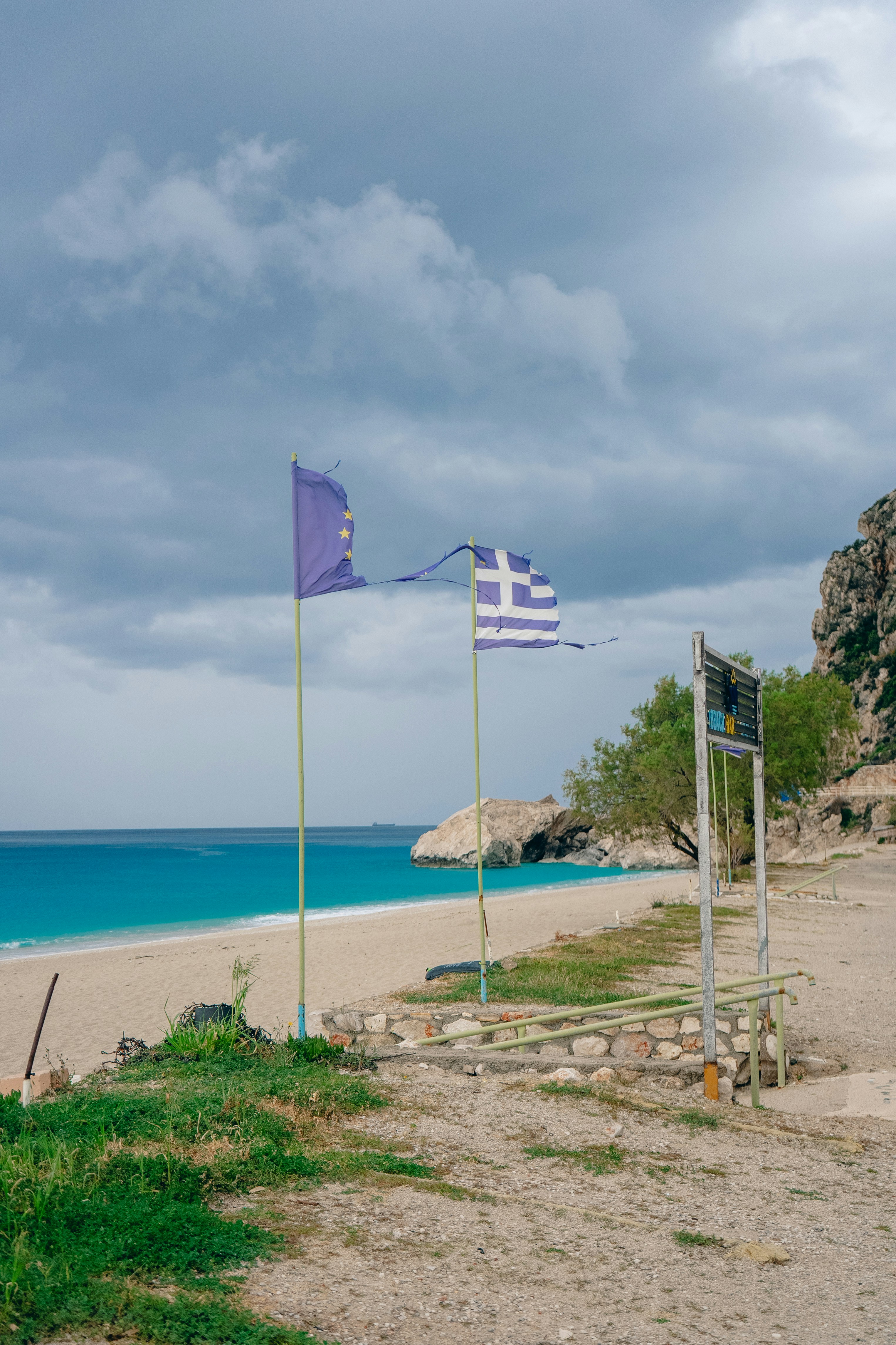Flagged shoreline: purple banners and turquoise sea at a sunlit Greek beach