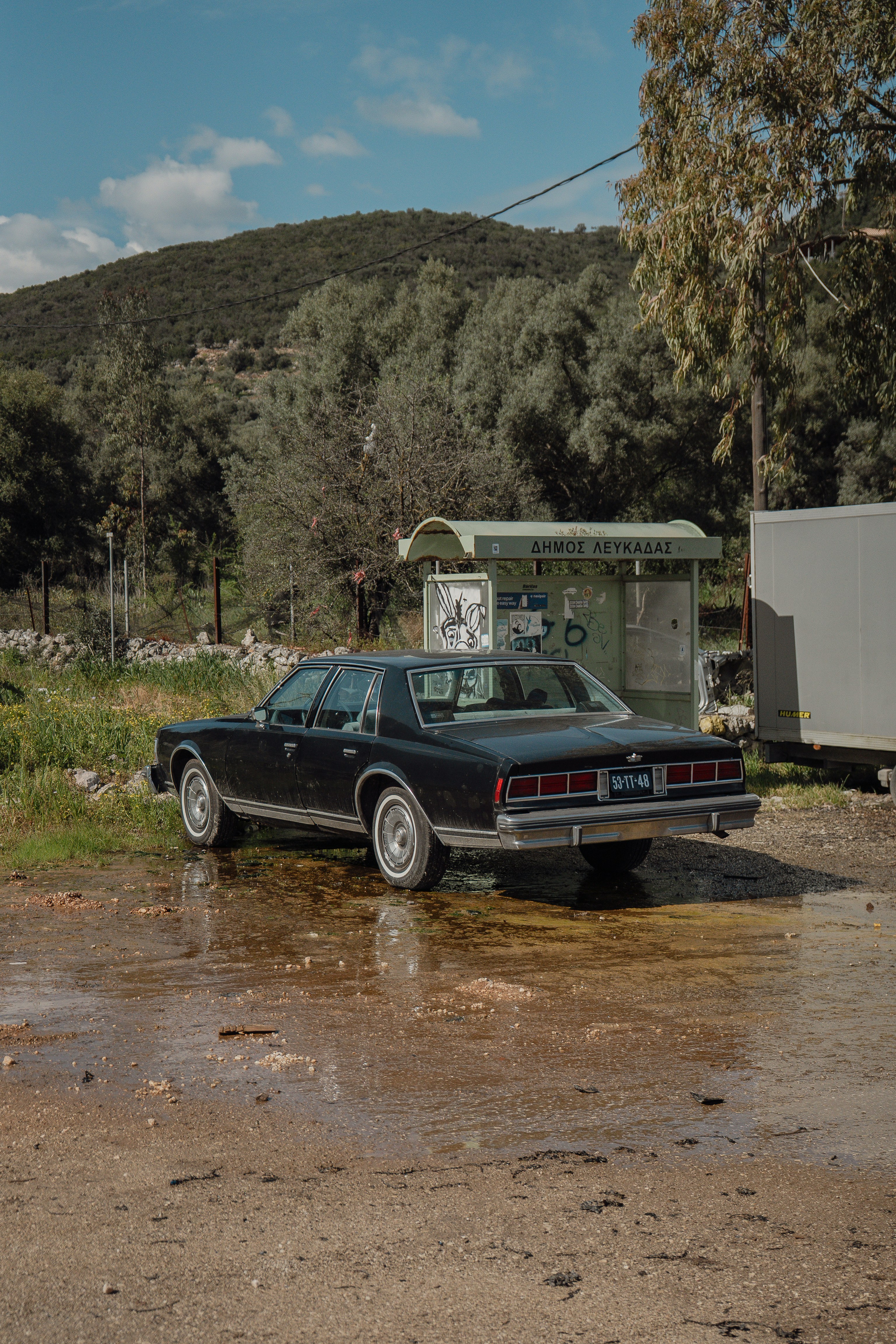 Midday Halt: A Vintage Sedan Resting by a Bus Stop'