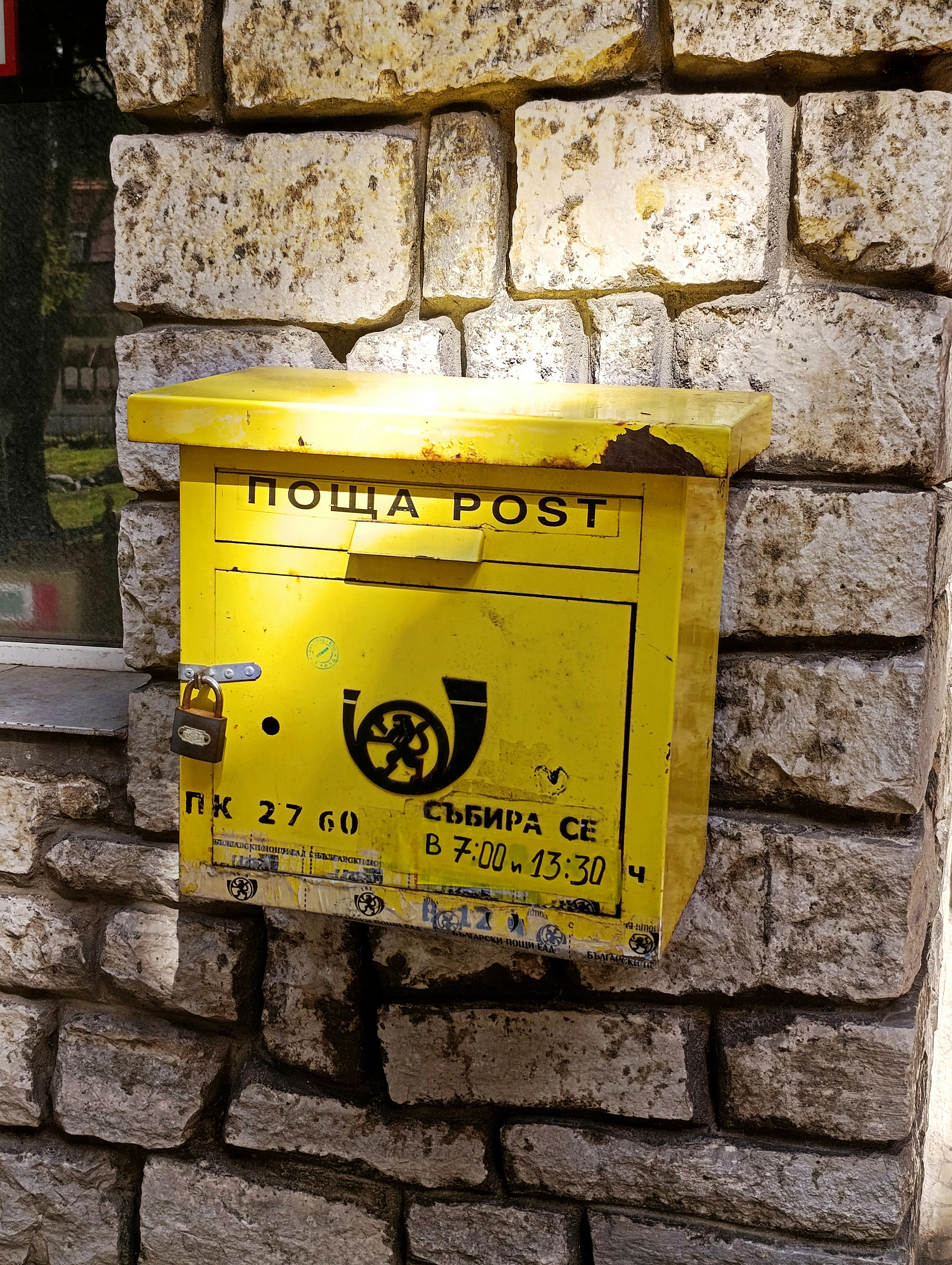 Sunlit Yellow Post Box Nestled in a Rough Stone Wall