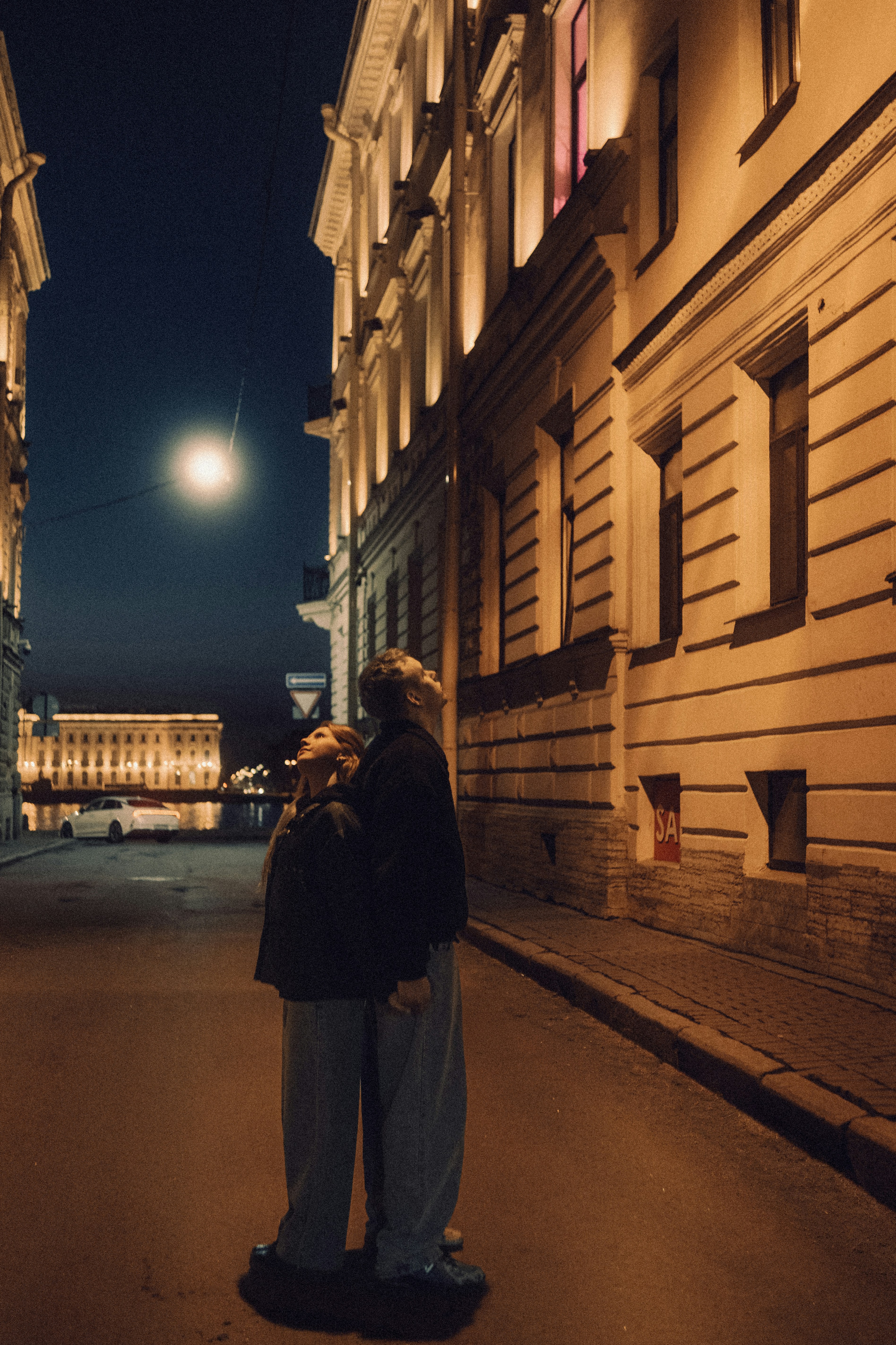 Nightfall in a Narrow Street: A Couple Reaches for the Sky