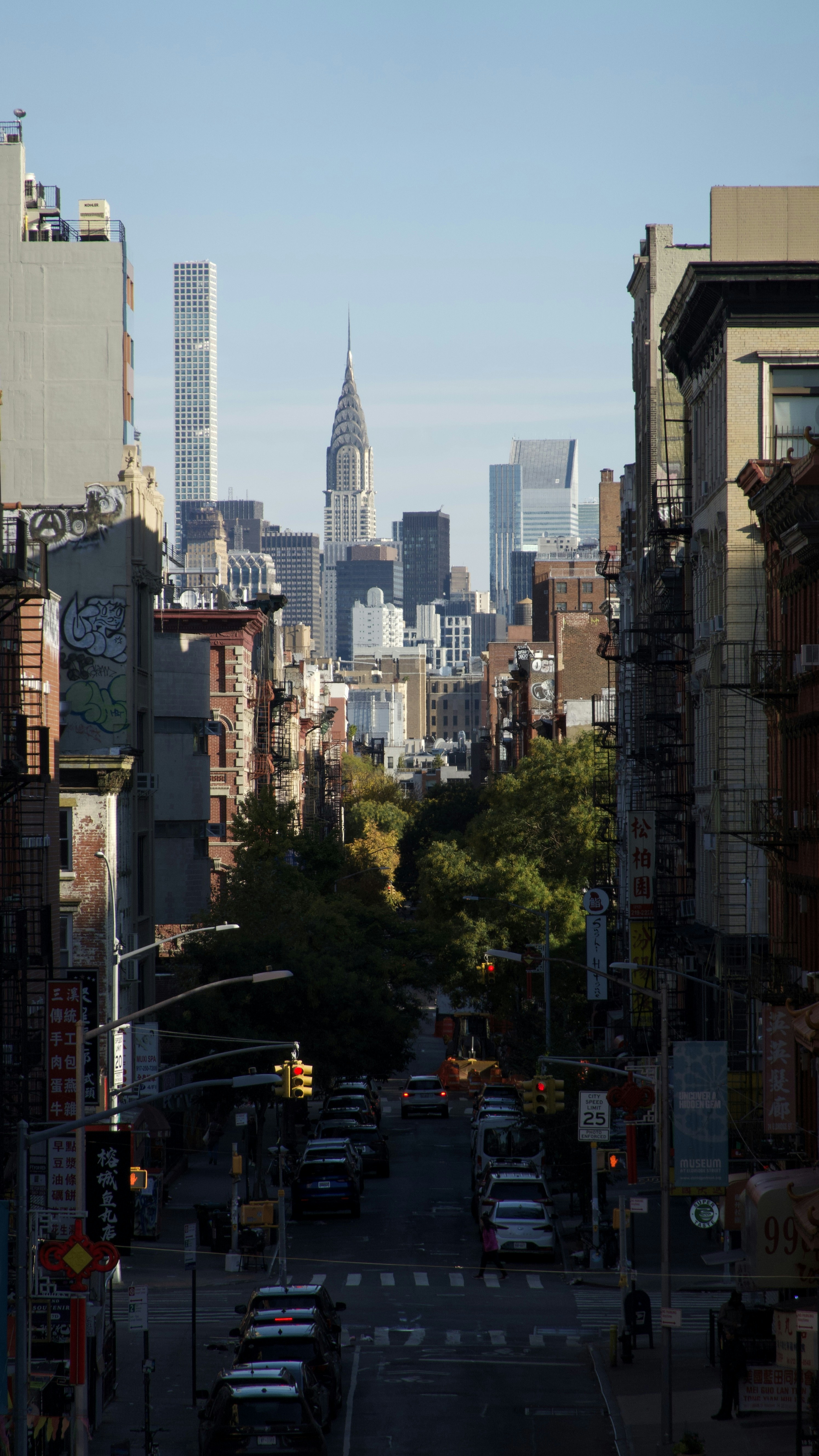 Chrysler-like tower peeking above a sunlit Manhattan street canyon