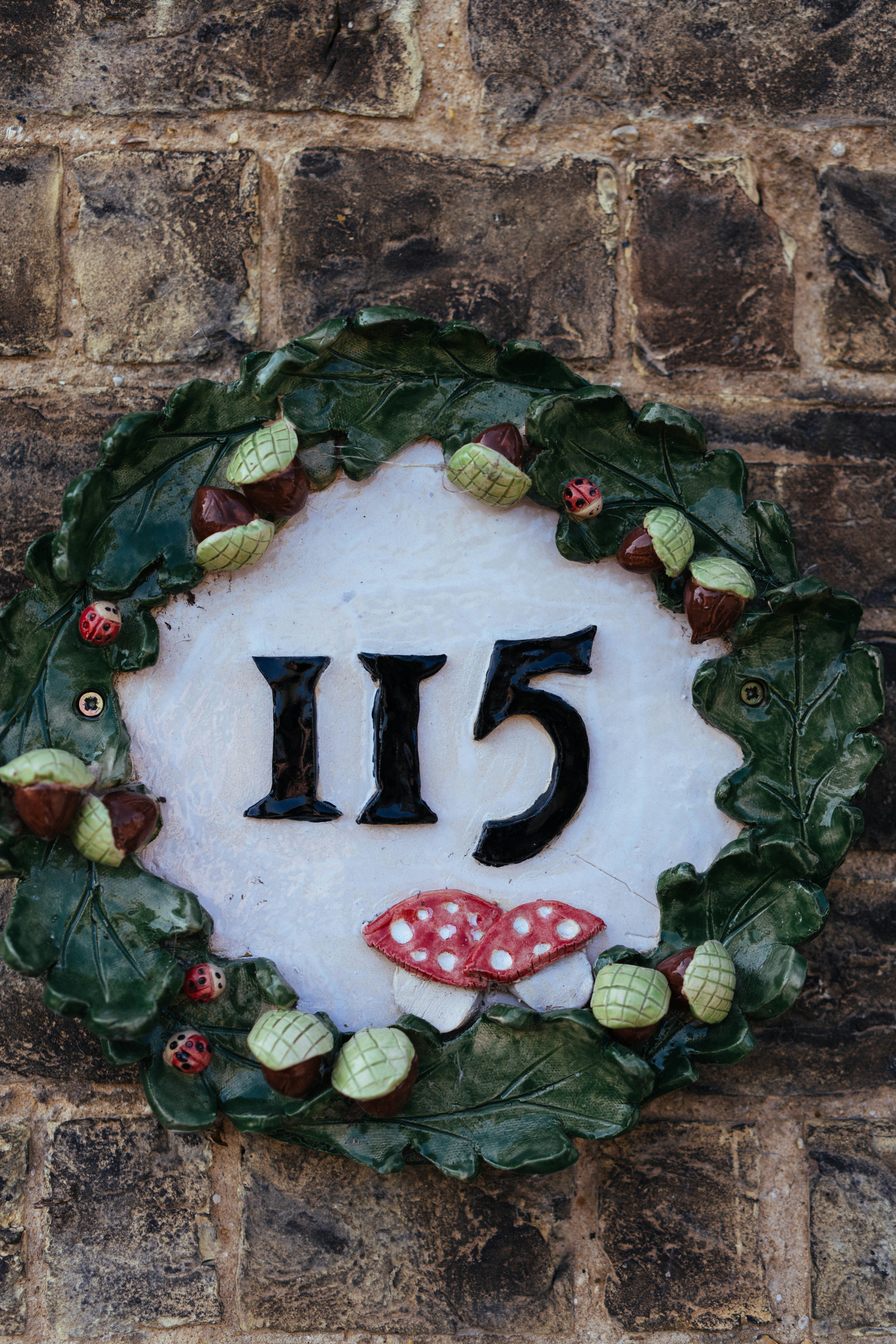 Number 115 in a decorative leafy plaque mounted on rustic brick wall