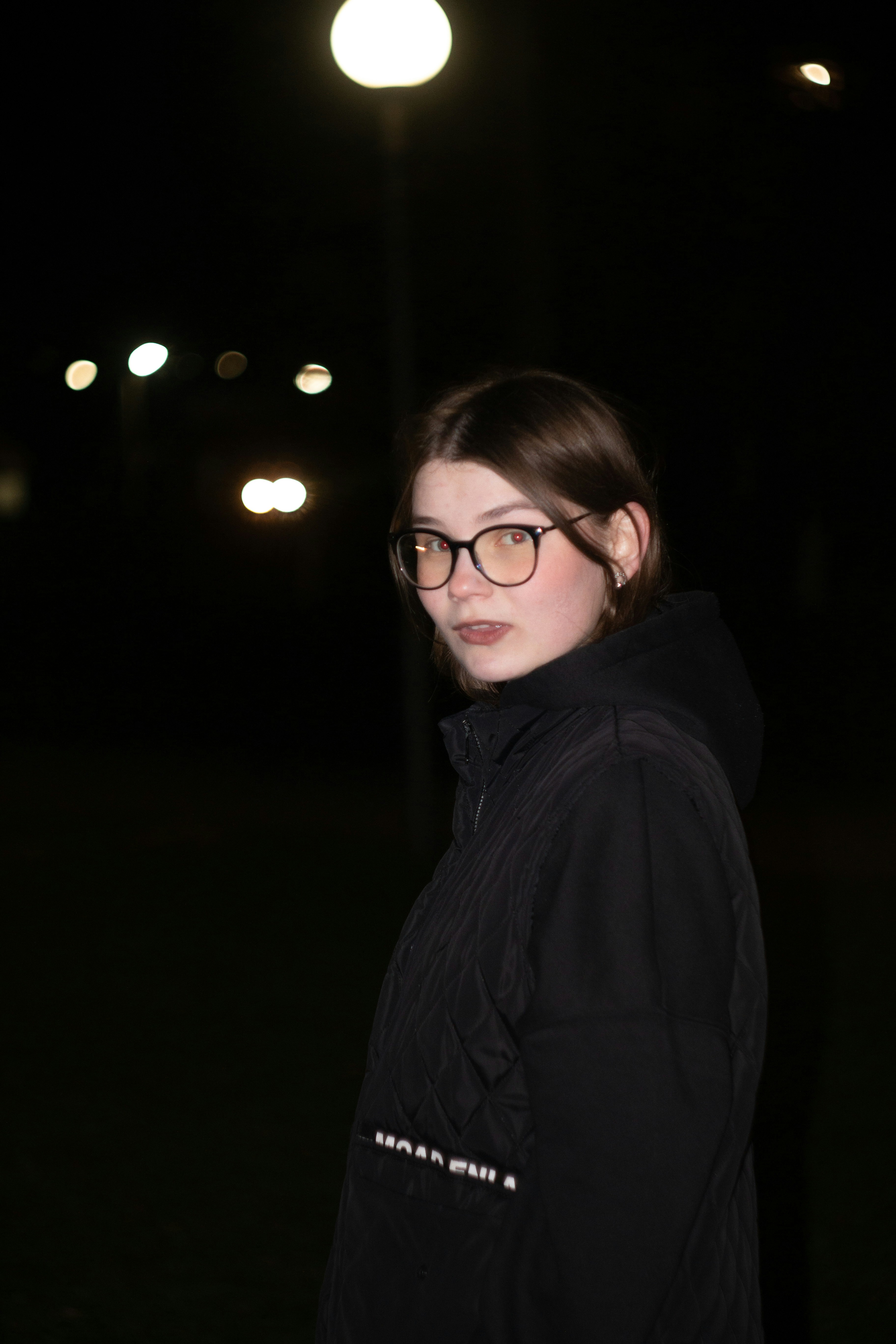 Night Portrait of a Young Woman in Glasses Under a Streetlamp