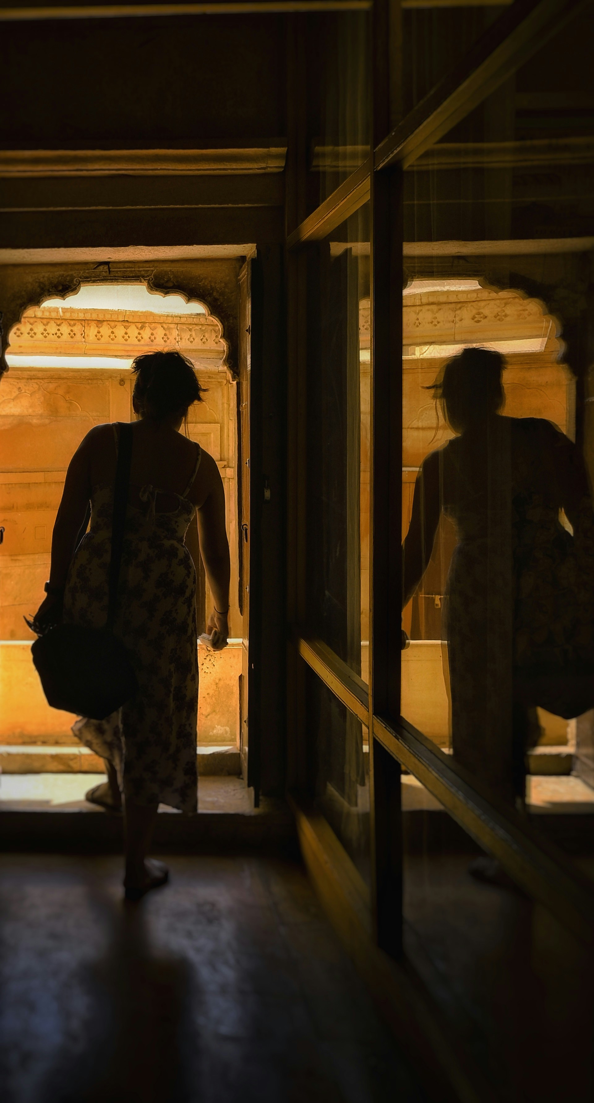 Shadowed Threshold: A Woman Steps Into Warm Carved Light