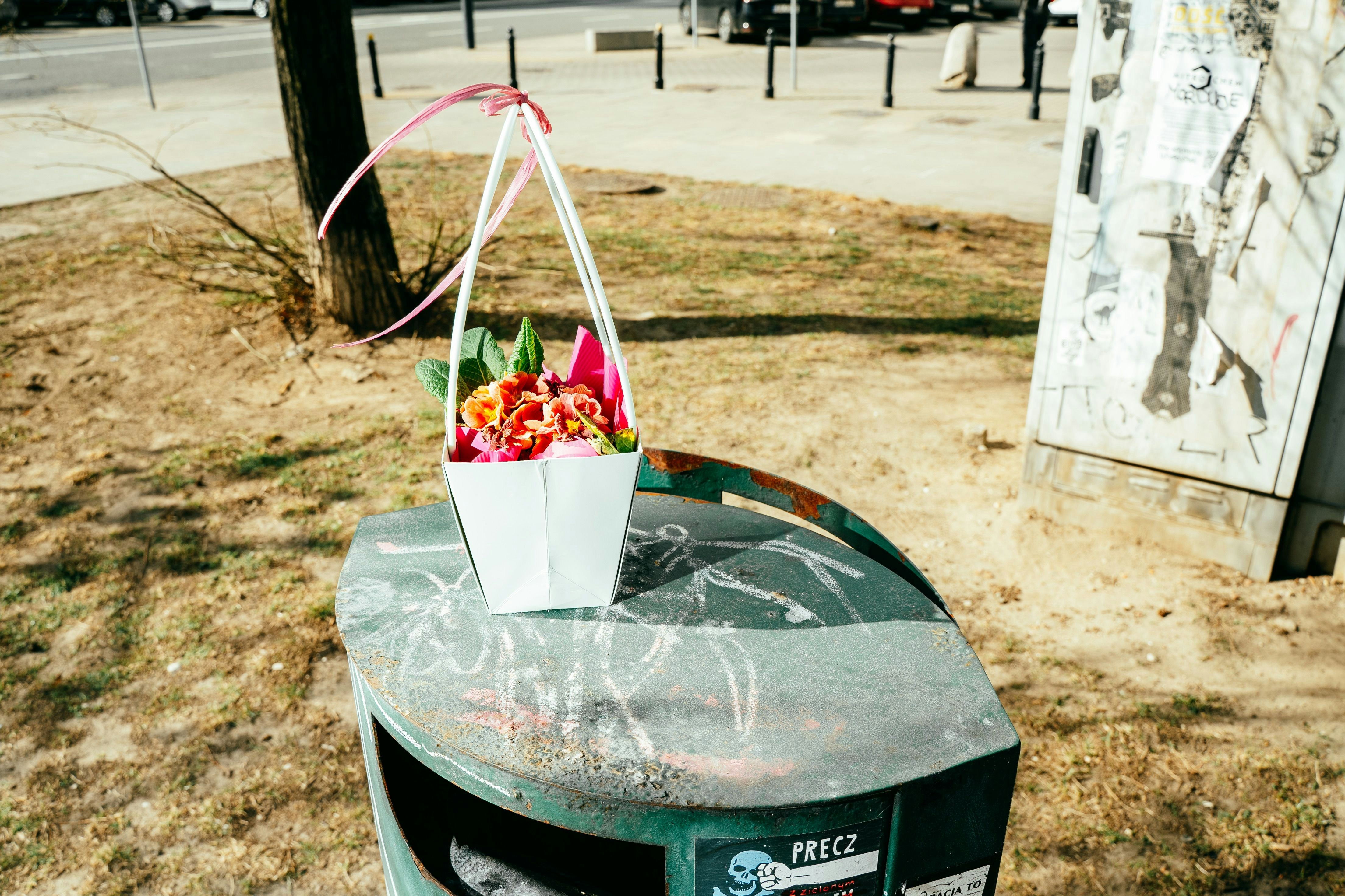 A single bouquet perched atop a weathered trash bin in a sunlit park edge