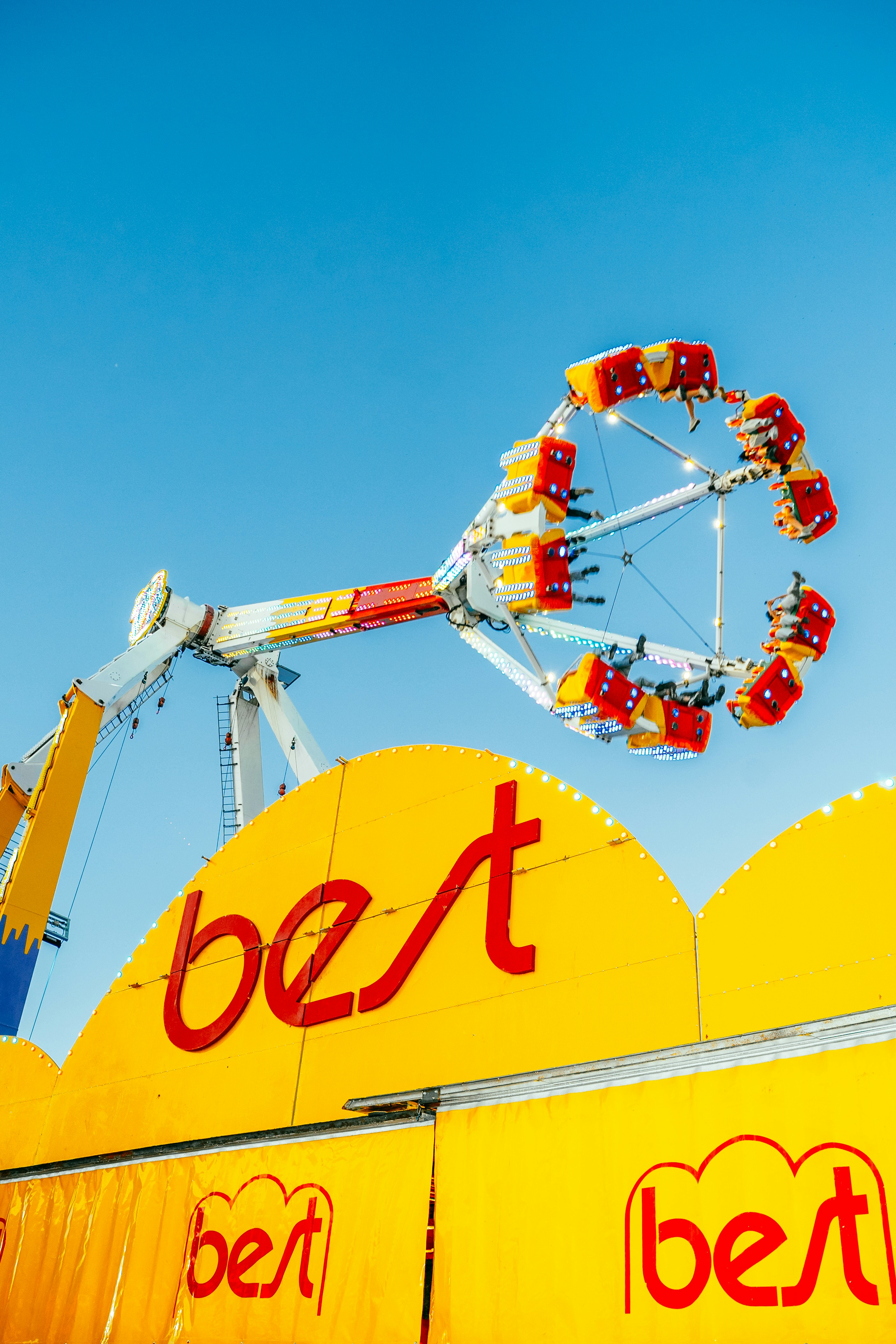 Yellow carnival signage beneath a looping ride under a clear blue sky