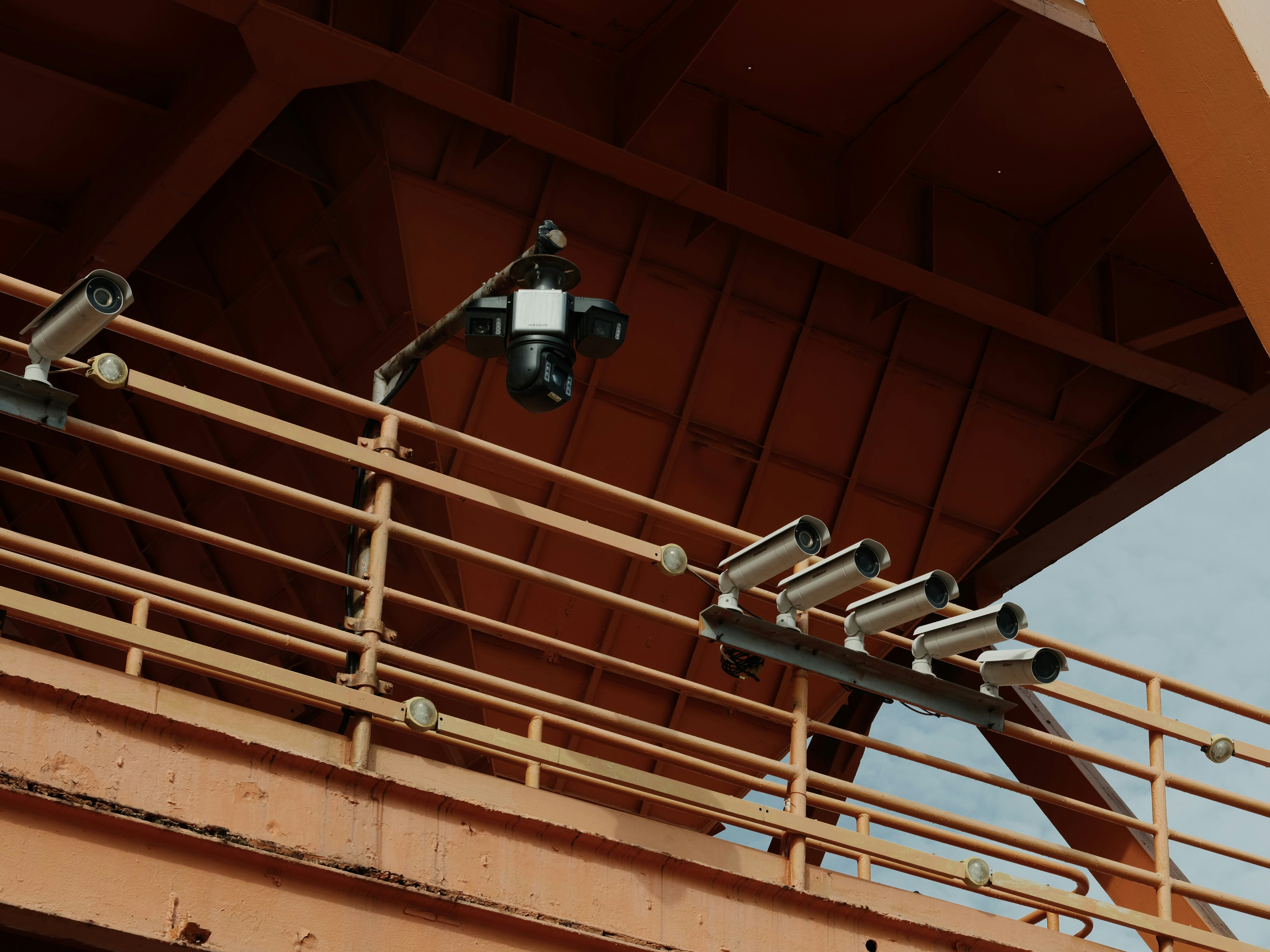 Camera Surveillance Over Orange Steel: A Mechanical Edge