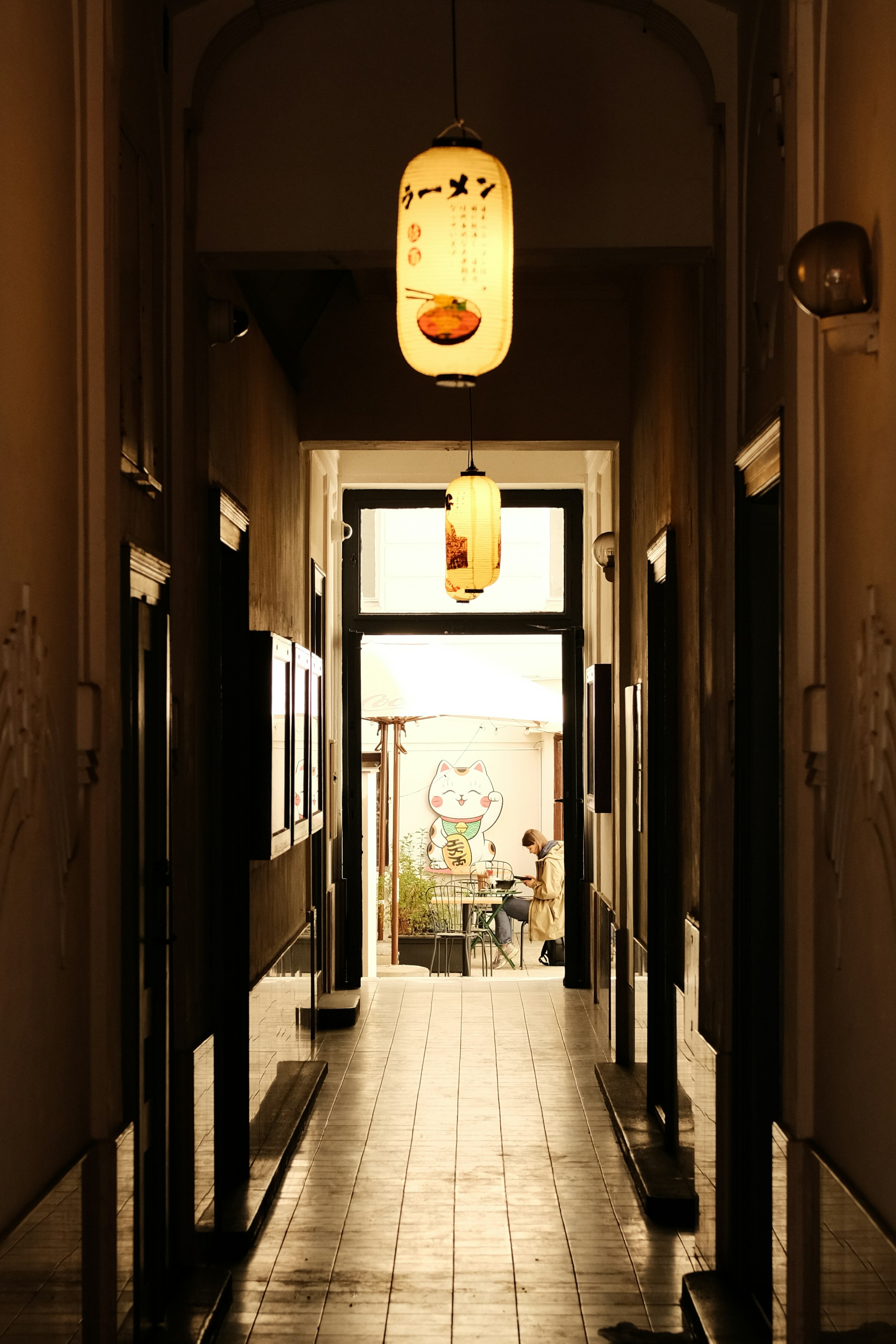 Lantern-lit Corridor to a Quiet Café with a Welcoming Cat Poster
