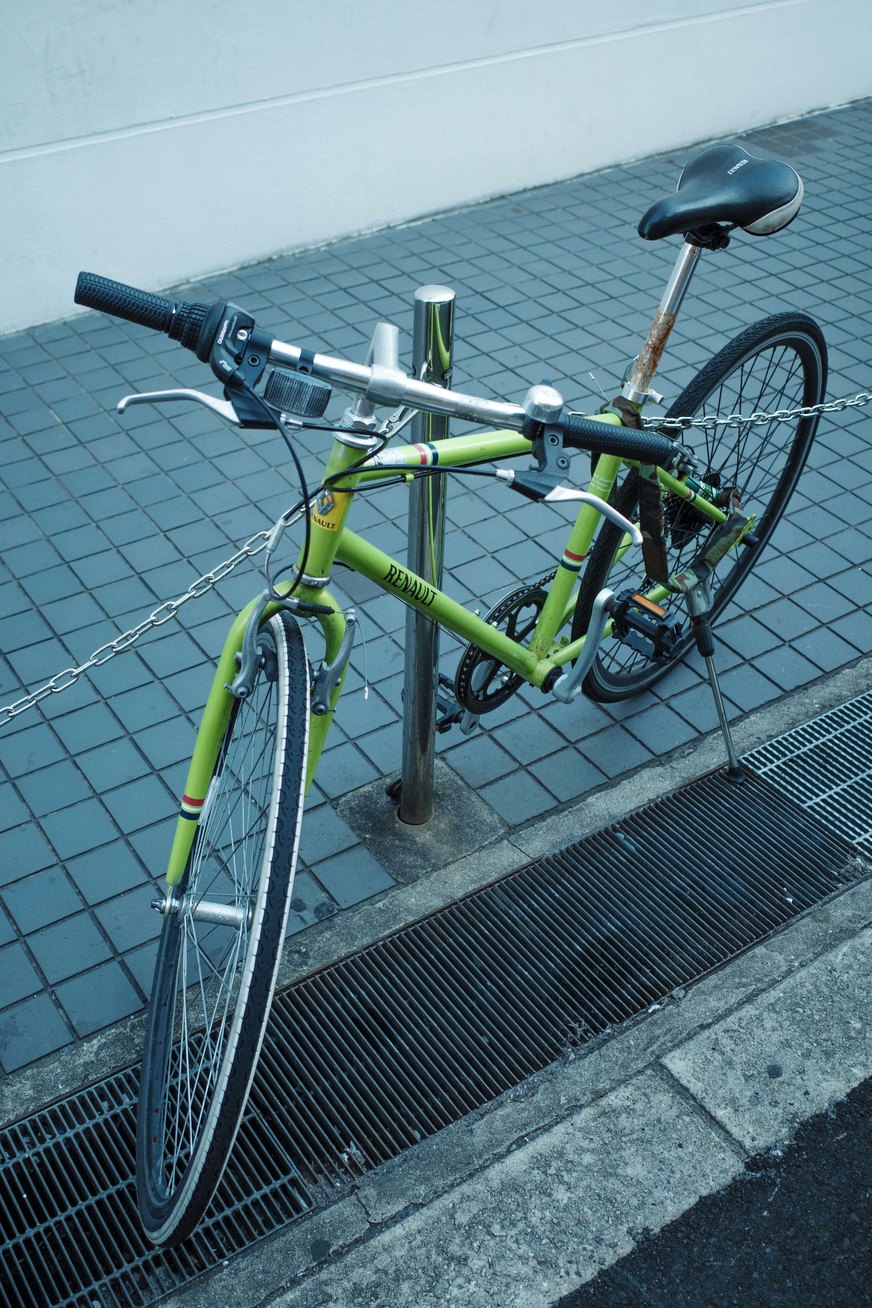Green Bicycle Locked to a Chain on a City Sidewalk